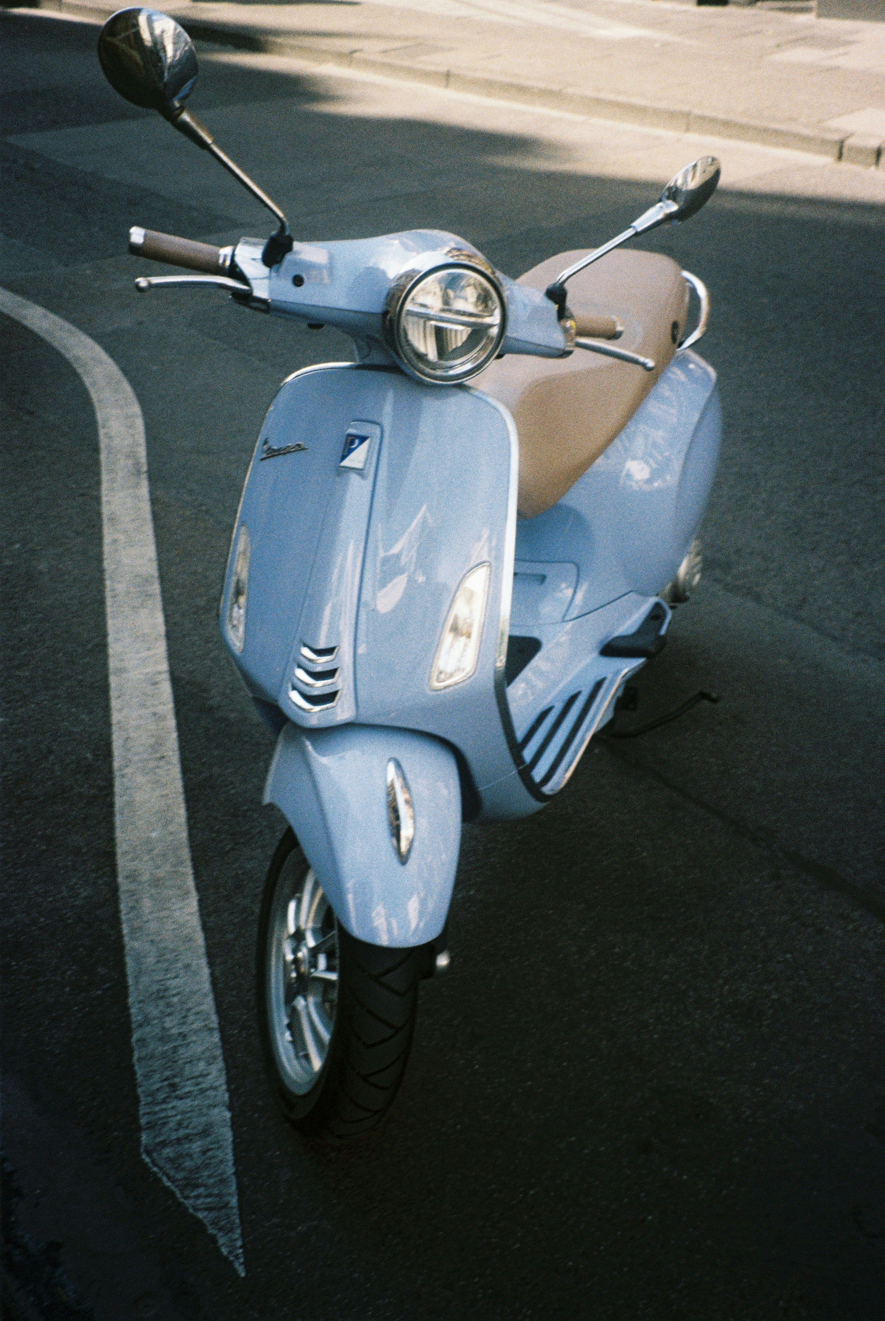 A vintage-style blue scooter parked on the street, showcasing its sleek design and chrome accents.
