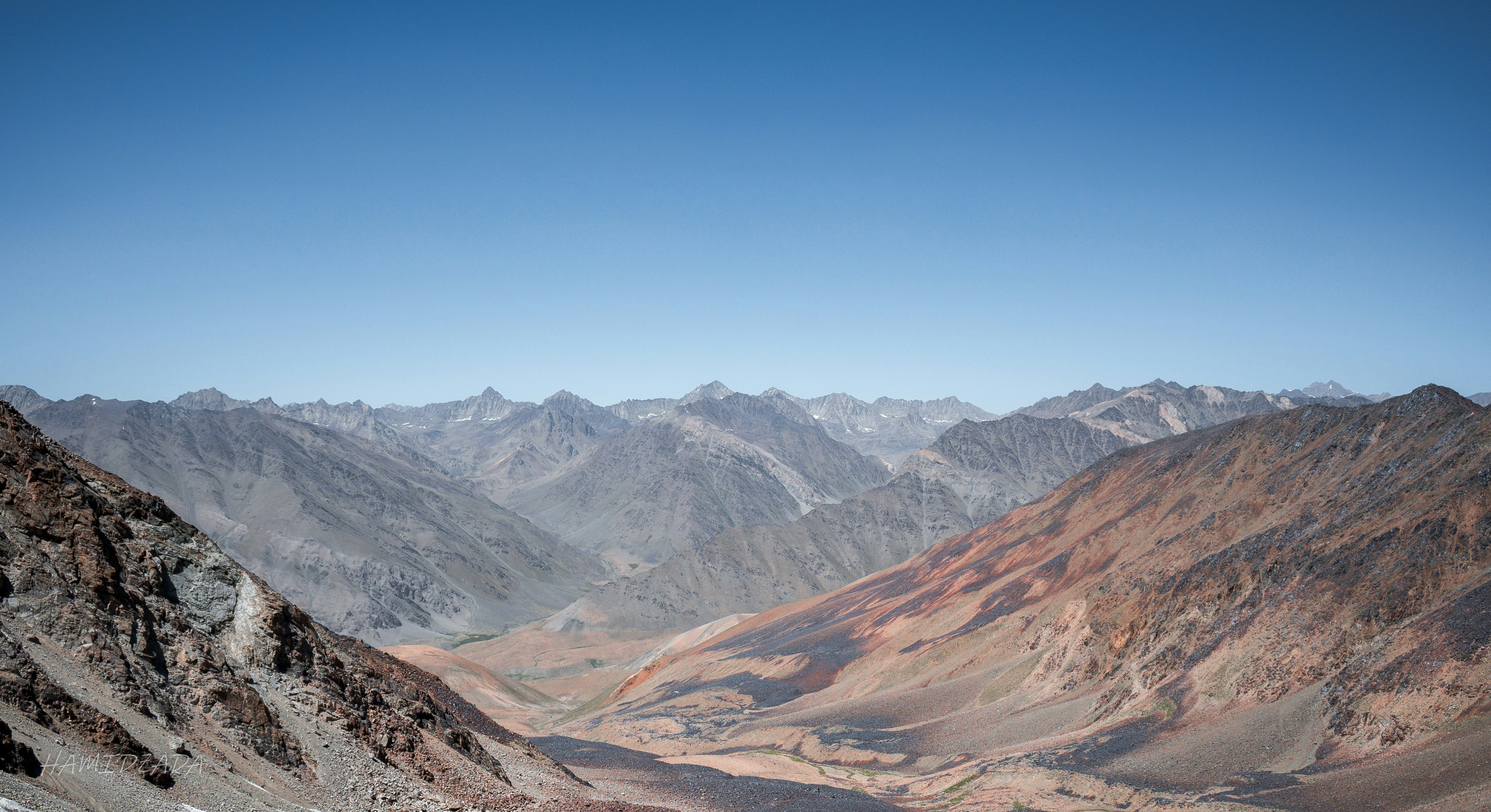 Expansive mountain range with rugged terrain and vibrant earth tones under a clear blue sky.