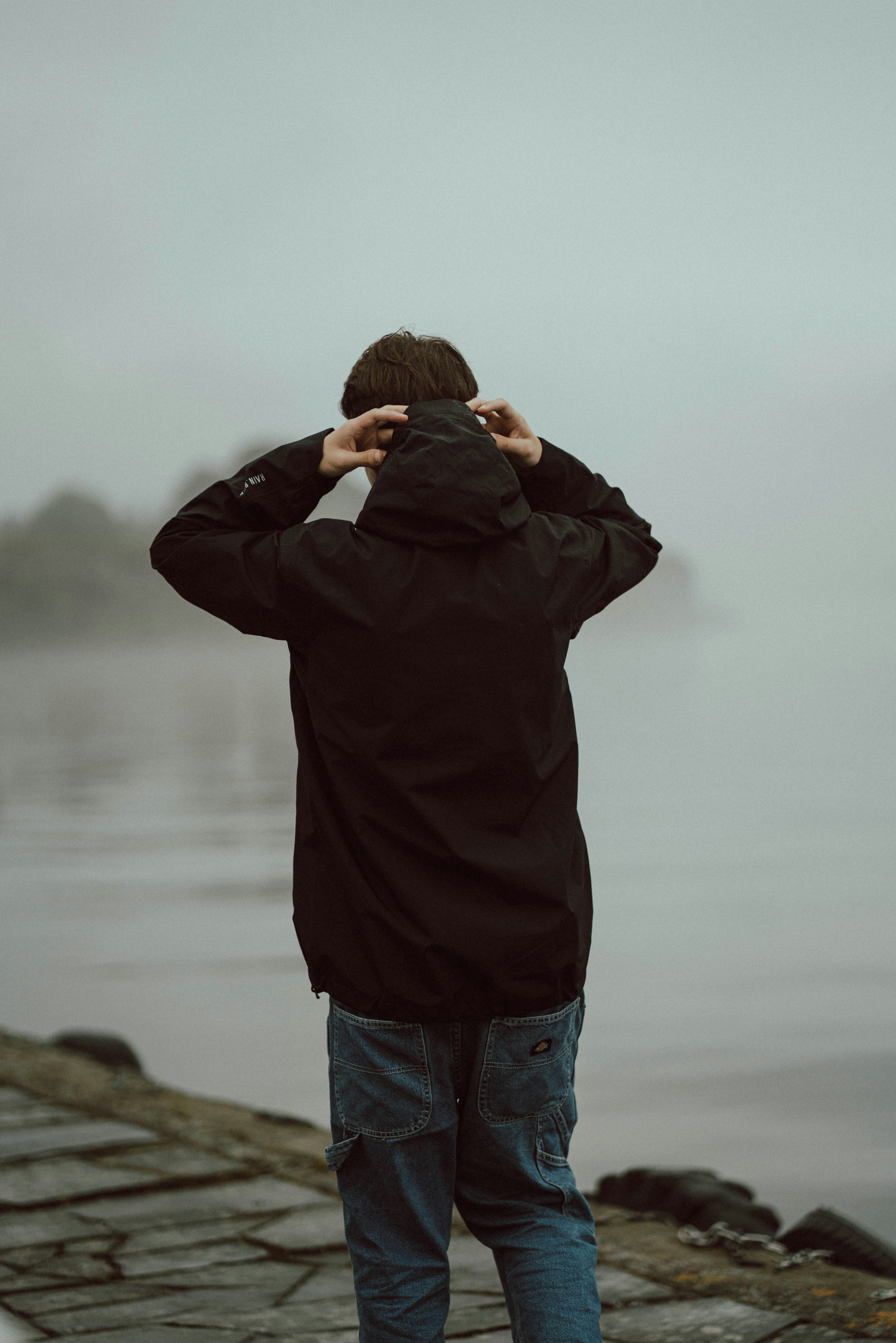 Person in black jacket adjusting hood by water