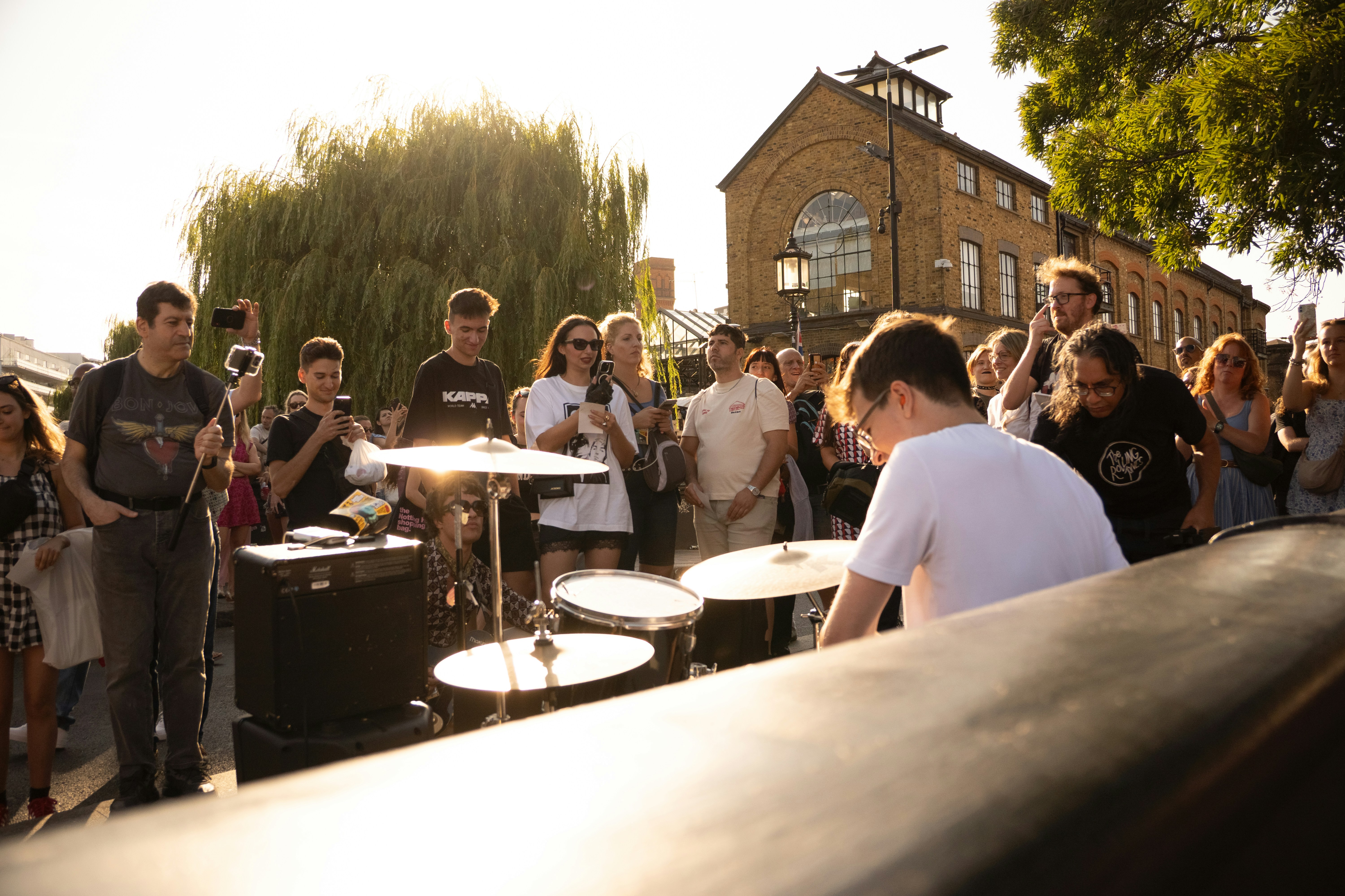 A drummer performs a street concert for a crowd in Camden Market. | Young drummer performs for an outdoor crowd