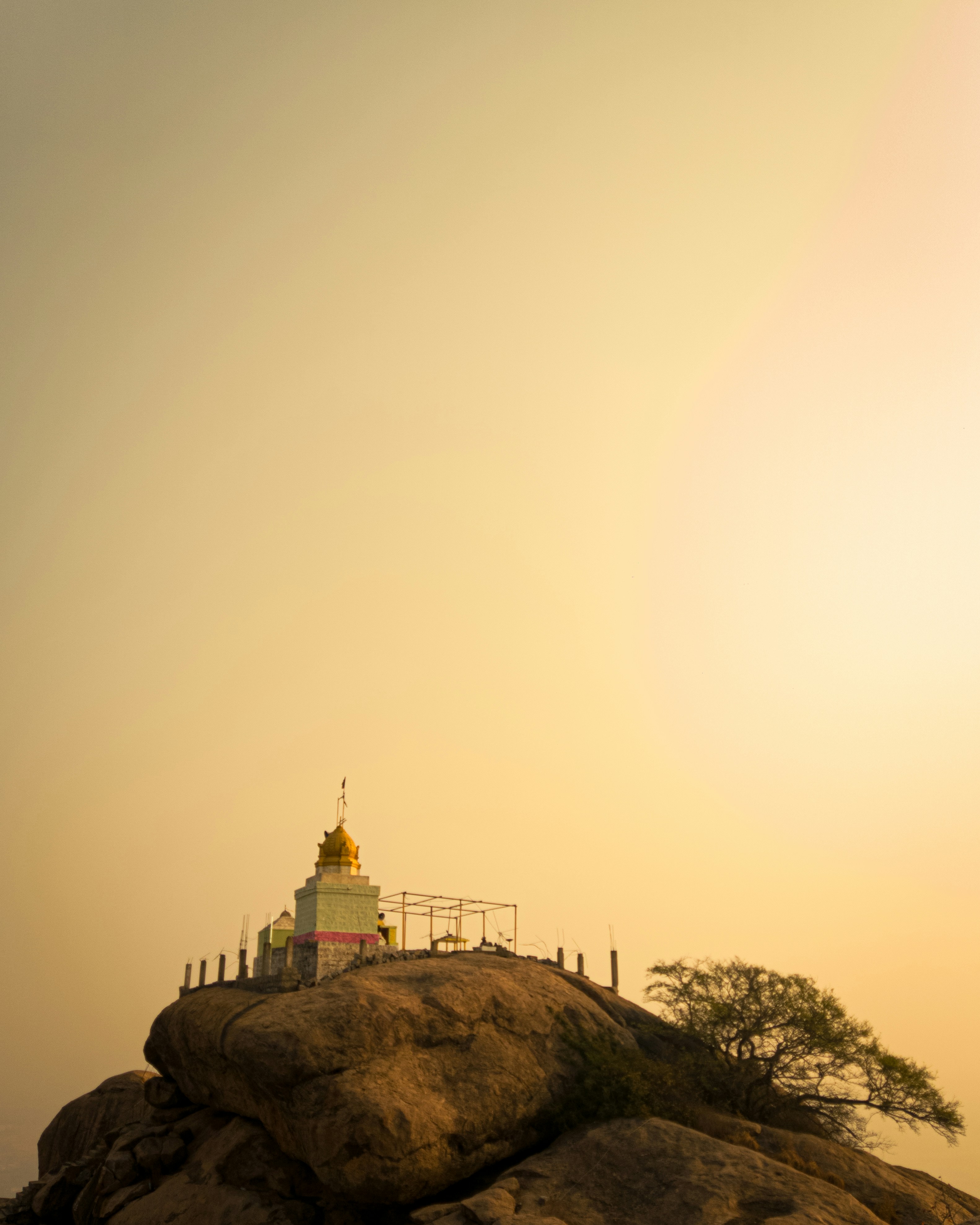 A golden-roofed temple perched atop a rocky outcrop, bathed in the soft glow of dusk. The horizon fades into a gentle gradient of warm hues.