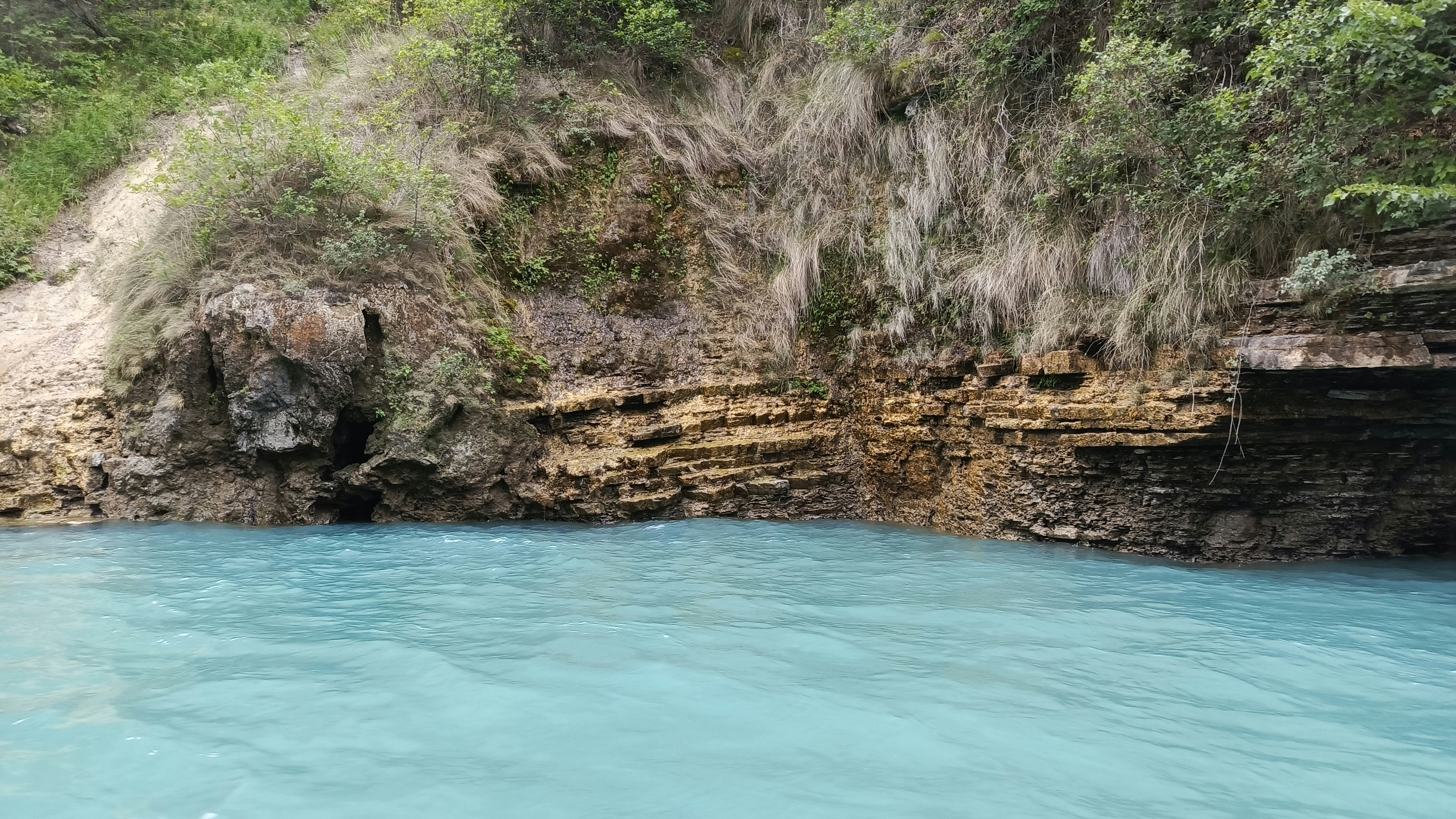 Turquoise water gently laps against rugged rock formations, framed by lush greenery along the shoreline.