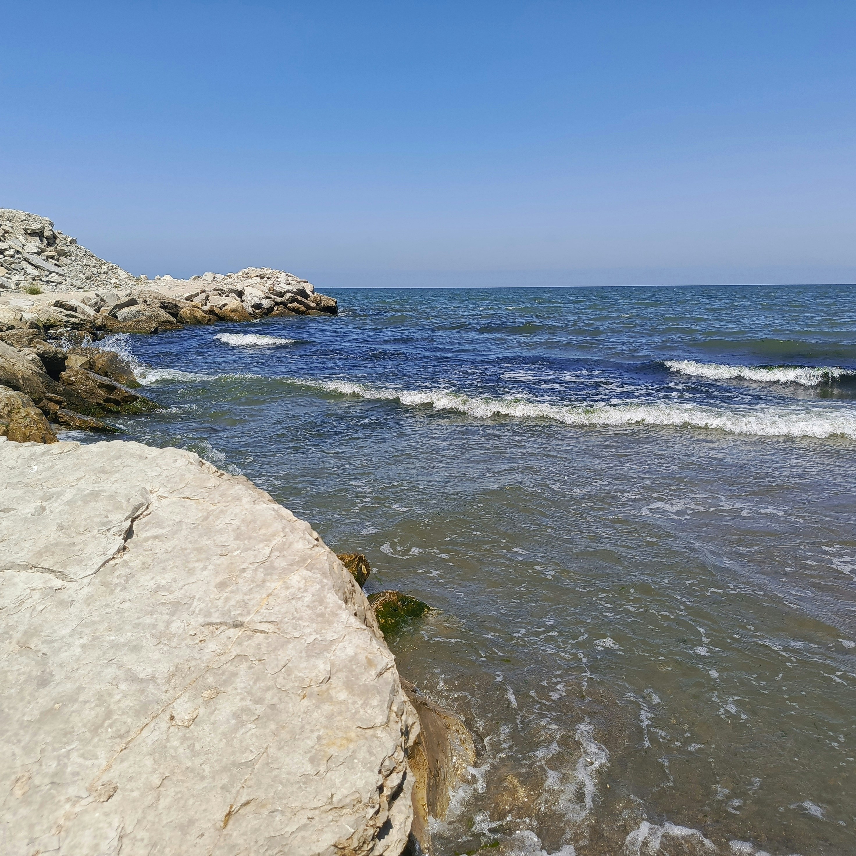 Waves gently crash on a rocky shore under a clear sky.