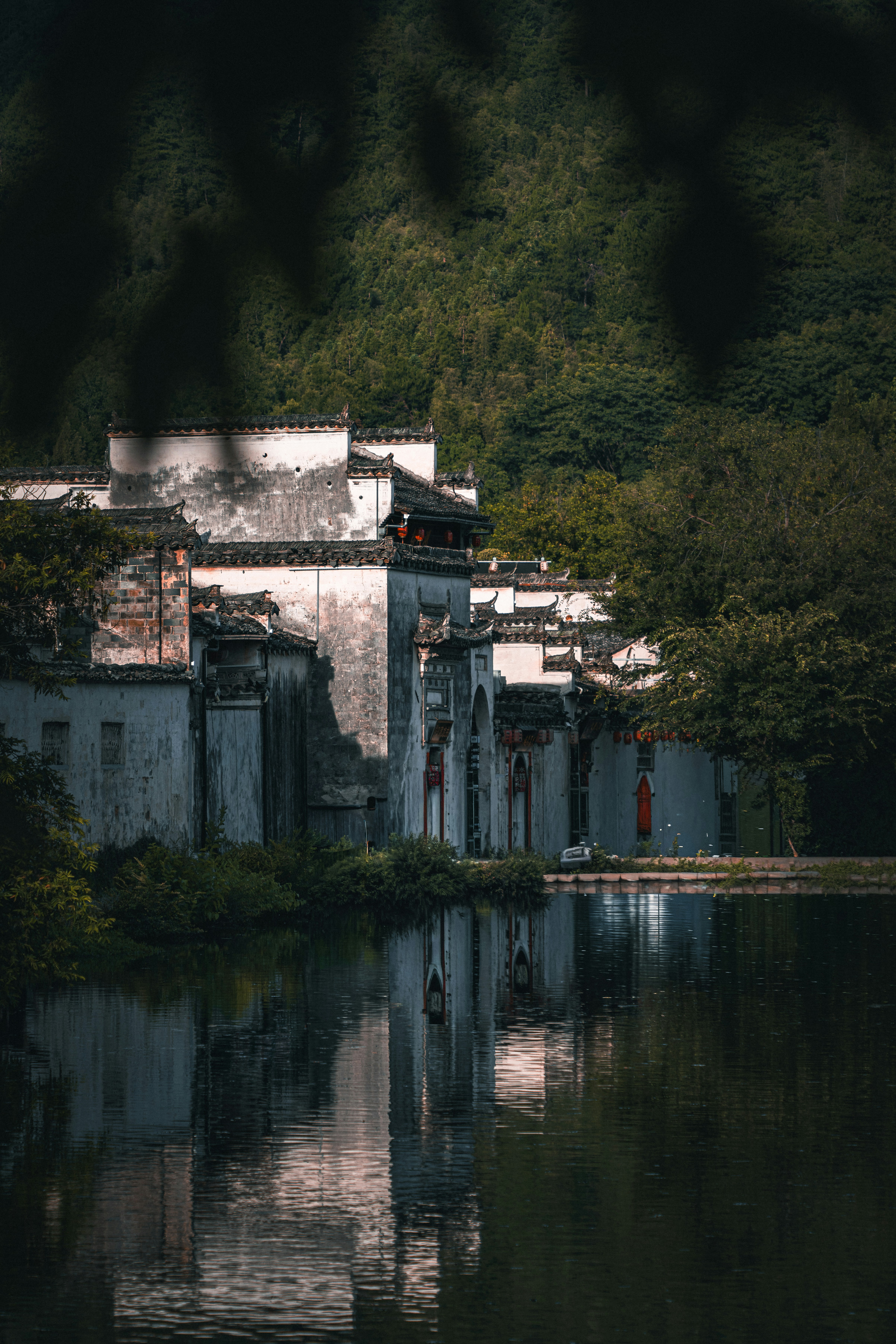 Historic architecture nestled by a tranquil lake, surrounded by lush greenery. The still water reflects the charming structures, enhancing the scene's timeless beauty.