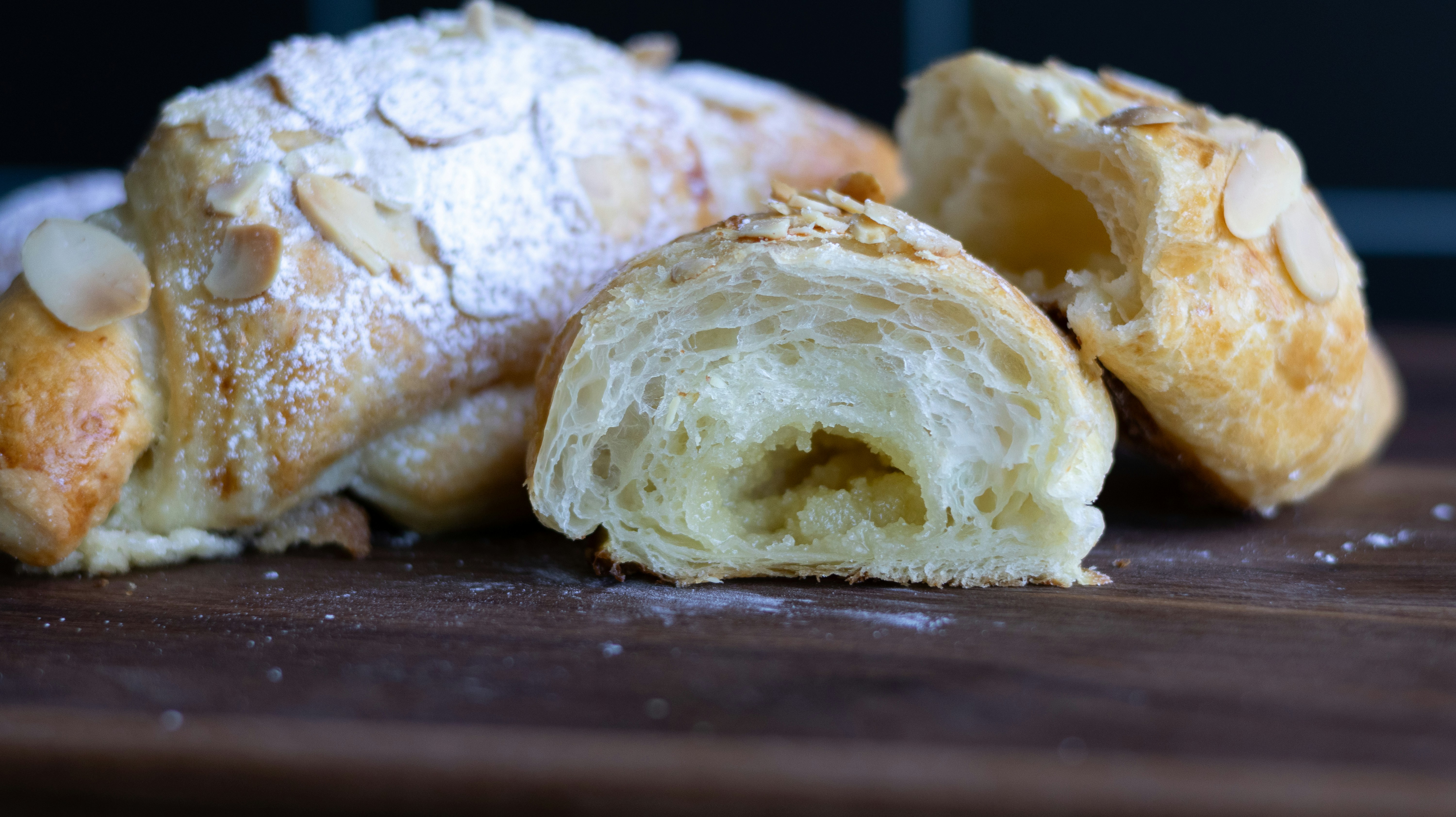A golden, flaky almond croissant, fresh from the oven. | Almond croissants dusted with powdered sugar.