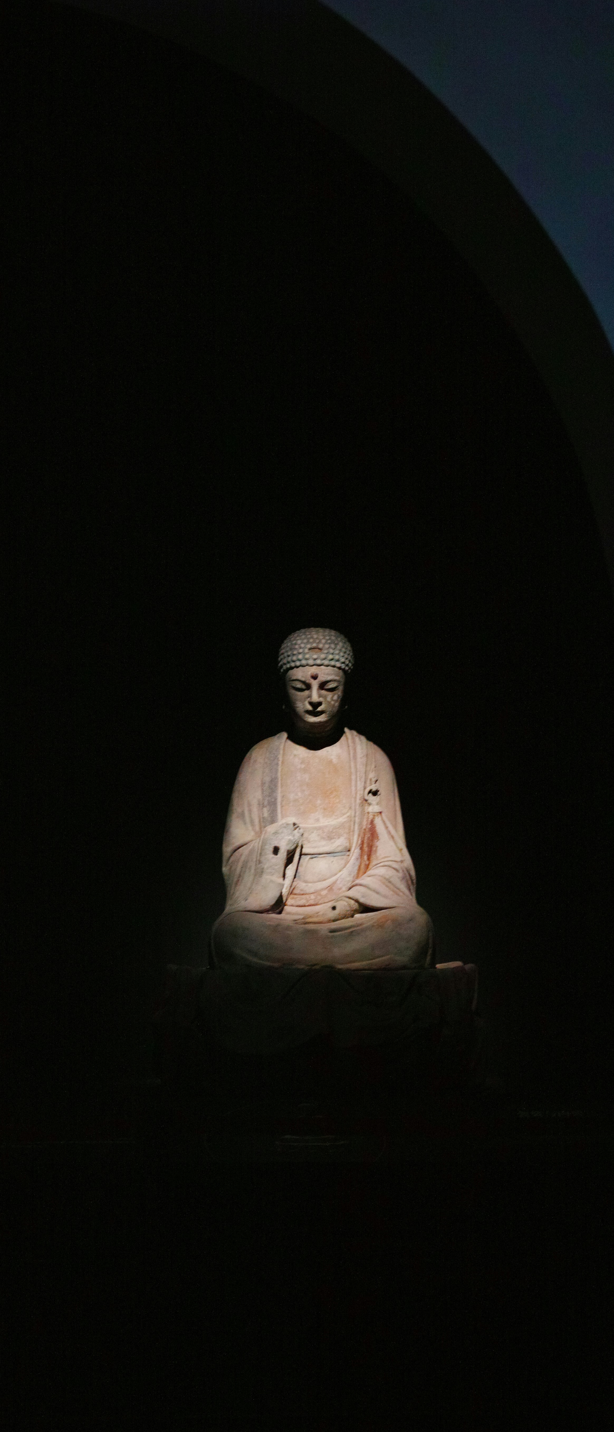 A stone statue of a meditating buddha in darkness