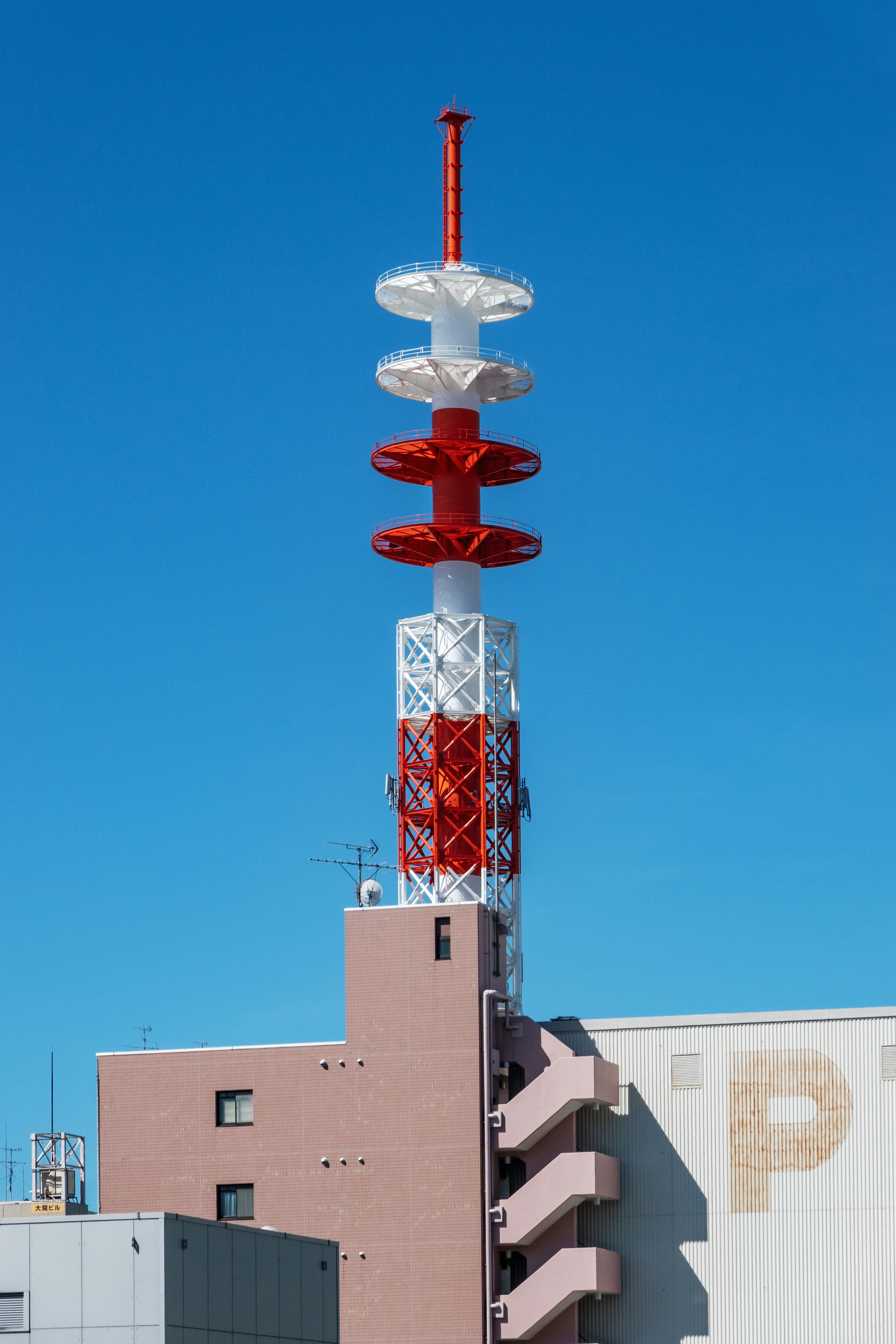 A tall red and white broadcast tower against a blue sky.