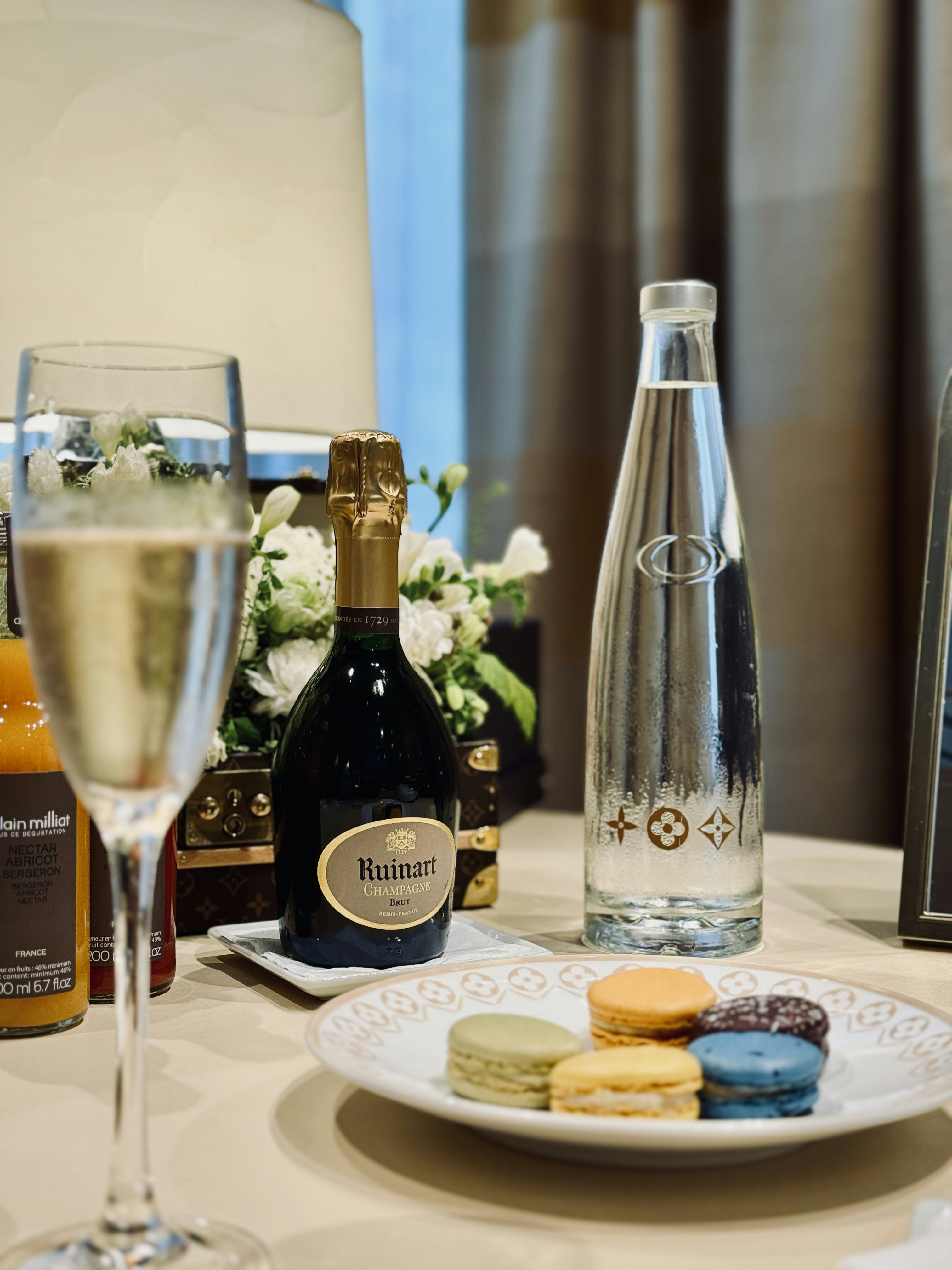 Bouteille de champagne, macarons et bouteille d'eau chez Louis Vuitton | Champagne, macarons, and water bottle on table