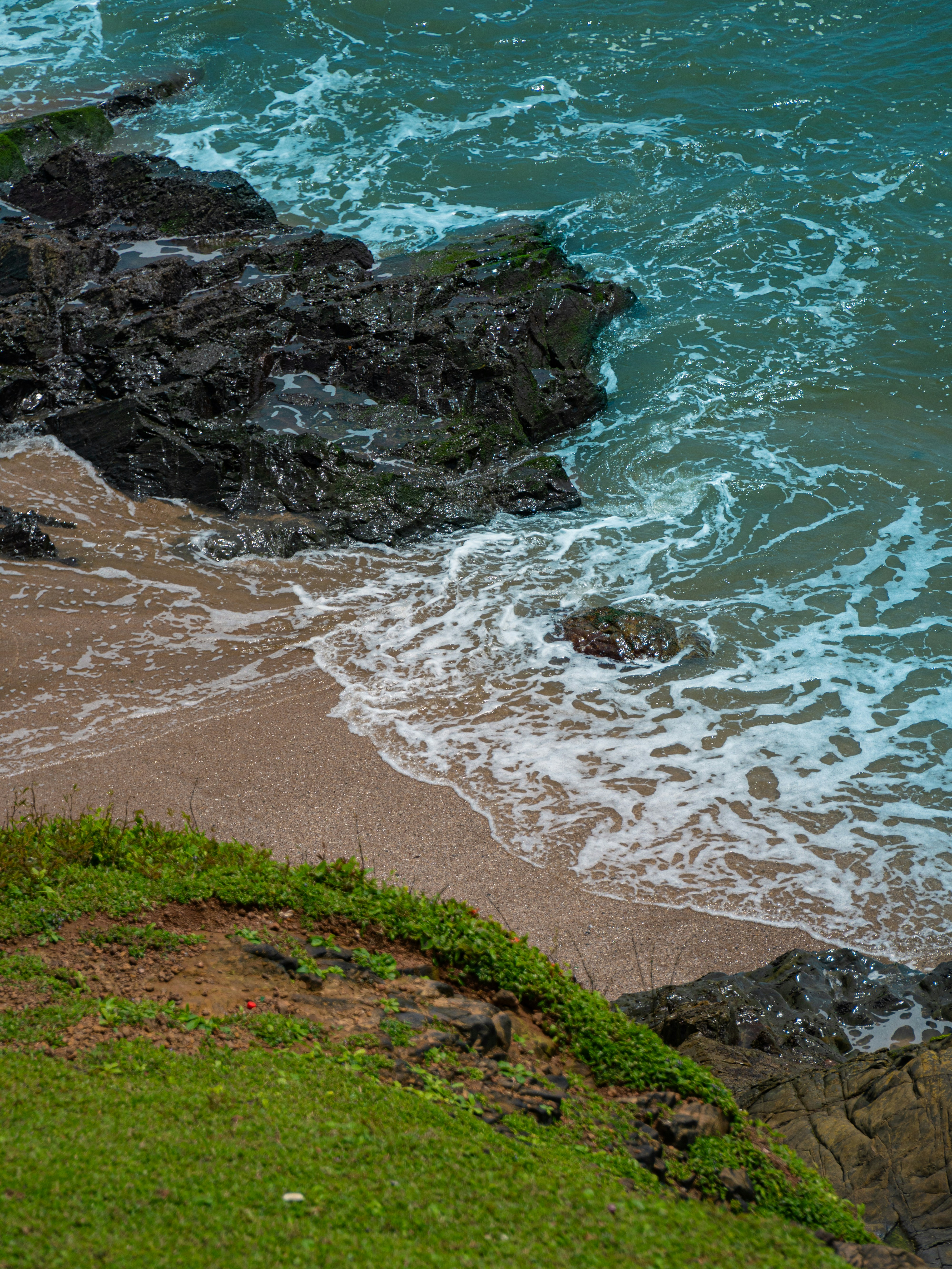 Waves crash on a rocky shore with green grass.