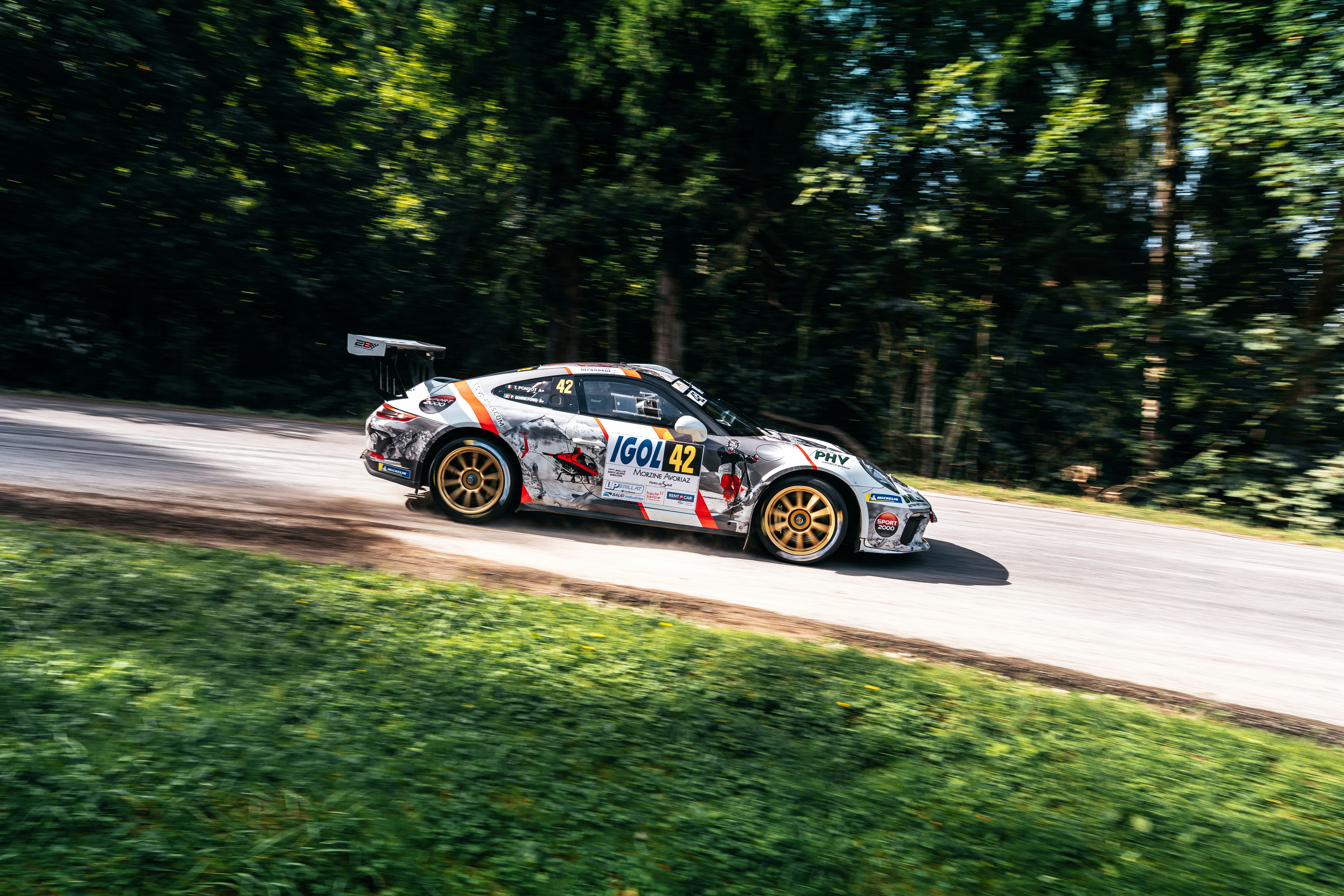 A race car maneuvering sharply on a winding road surrounded by lush greenery, showcasing speed and precision.