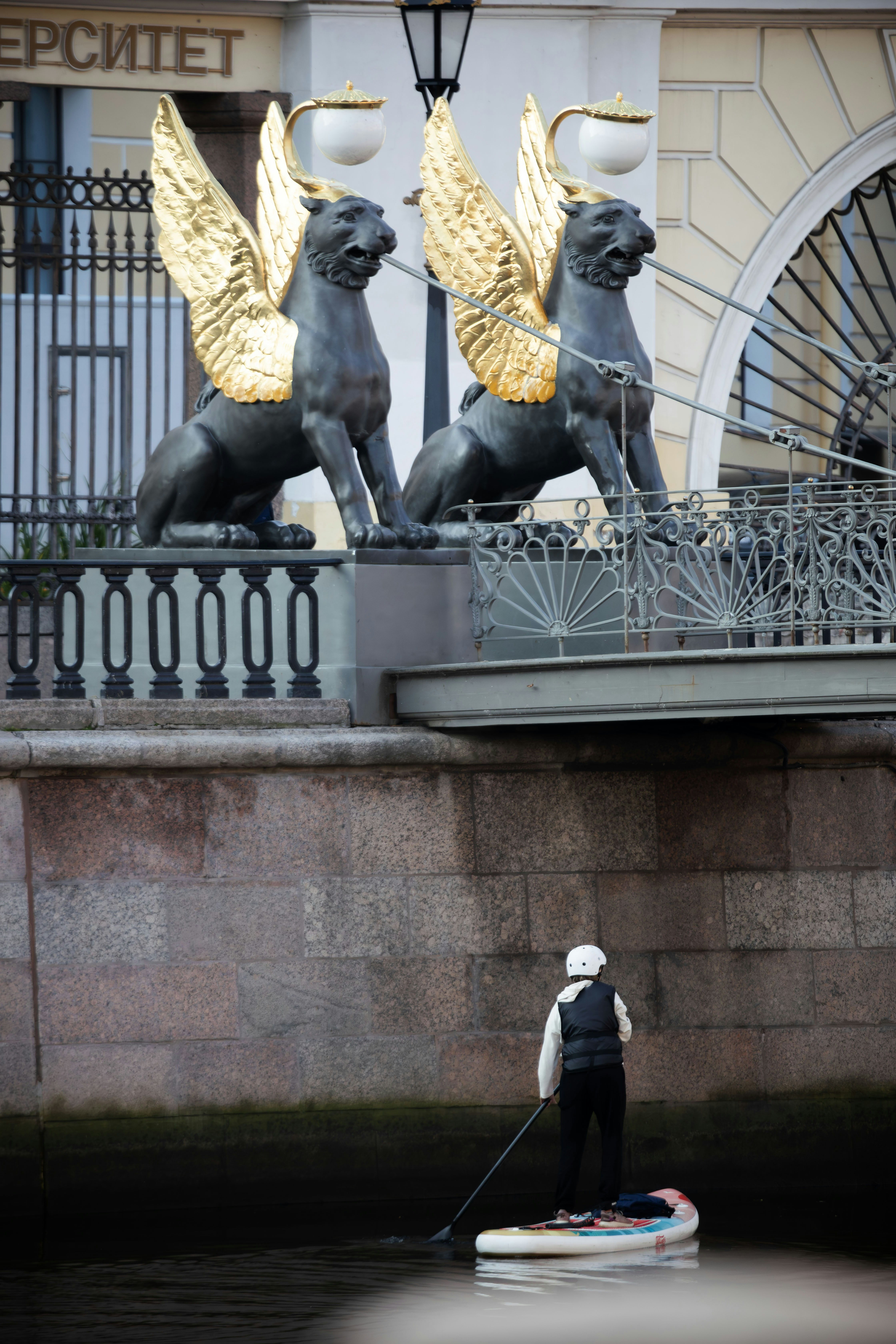 Gilded Griffins Over a Quiet Canal, with a Paddleboarder Below