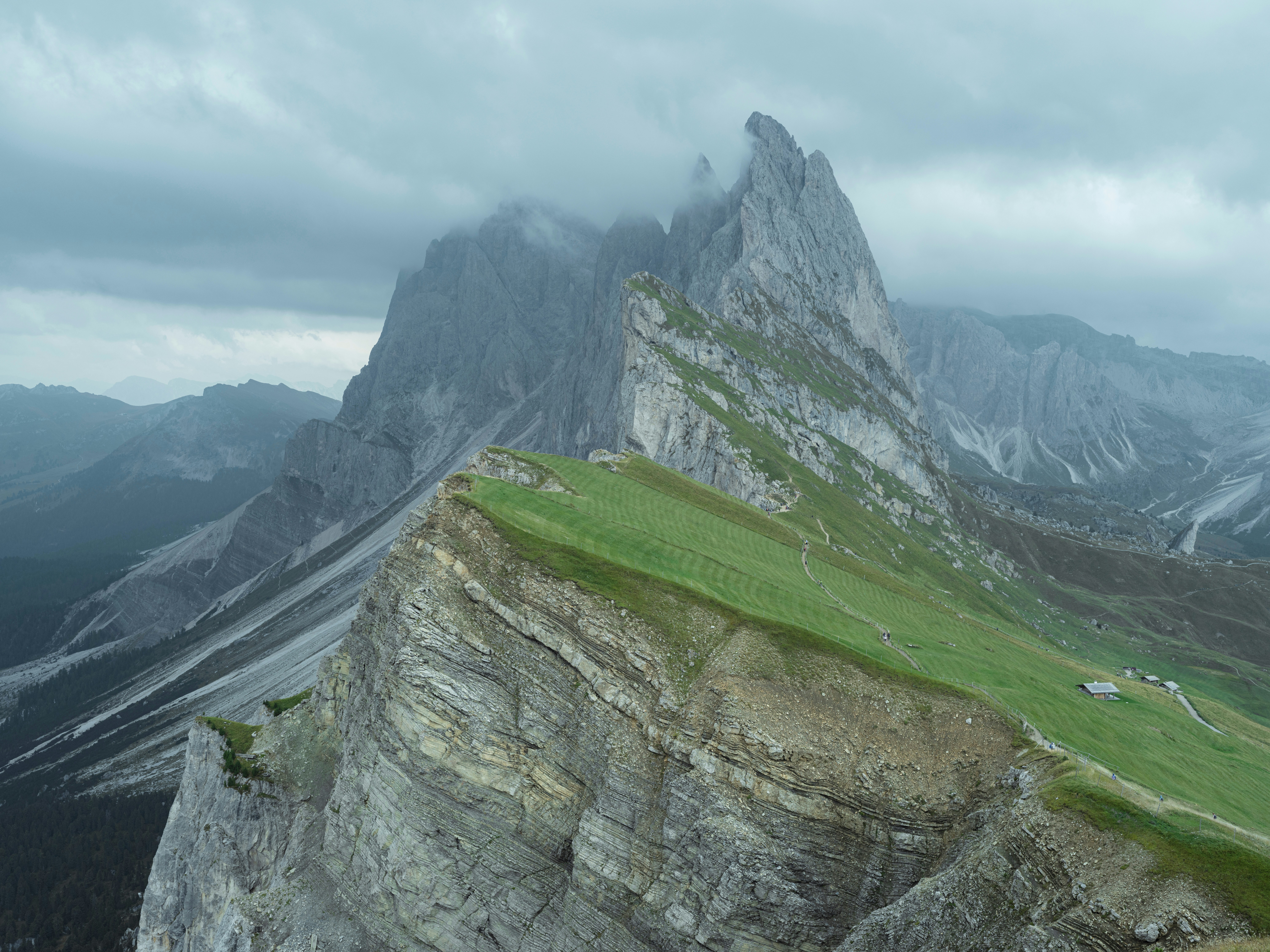 Majestic mountain range enveloped in mist, showcasing dramatic cliffs and lush green slopes beneath a cloudy sky.