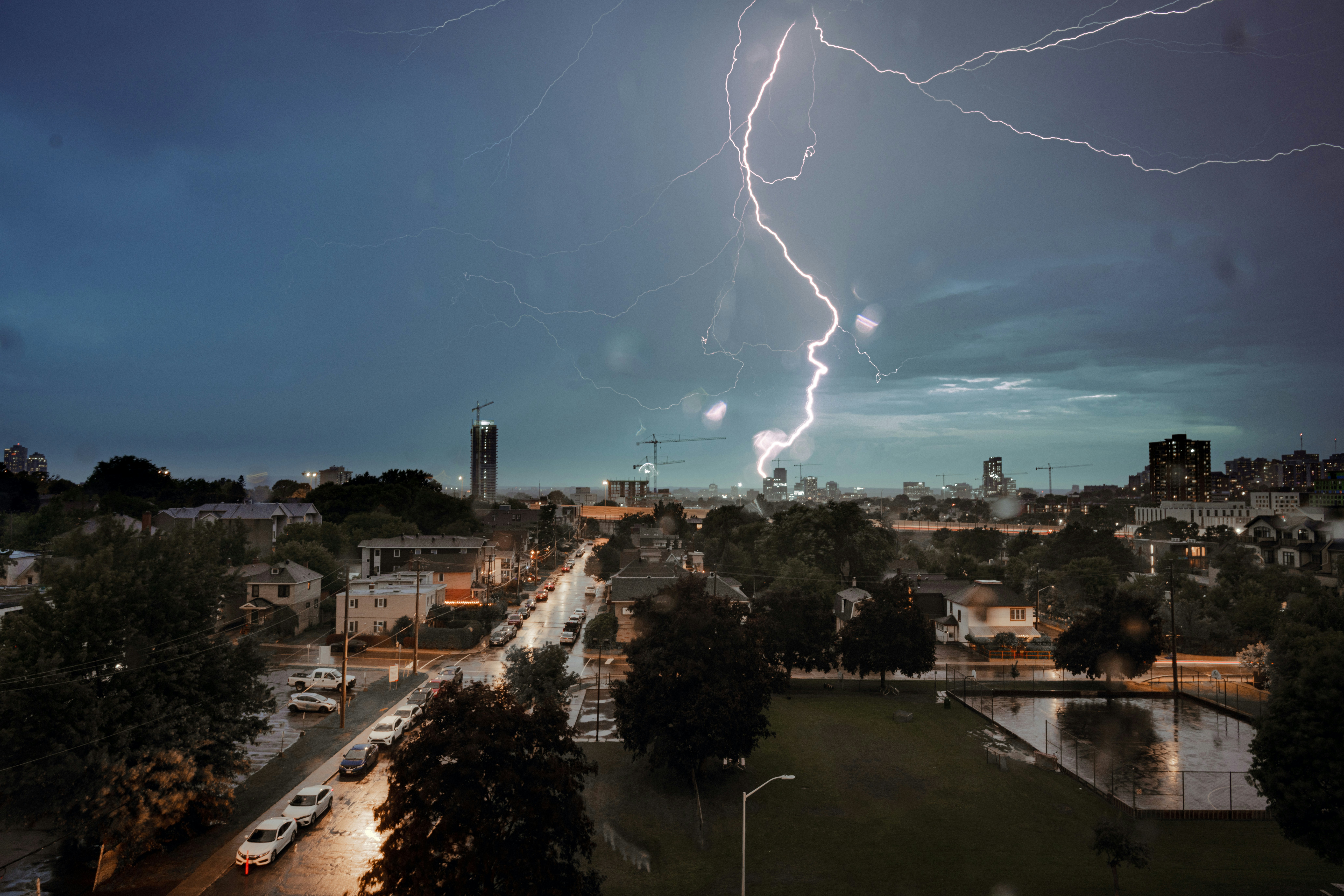 Lightning bolt striking a city skyline during a storm, illuminating the darkened sky and wet streets below.