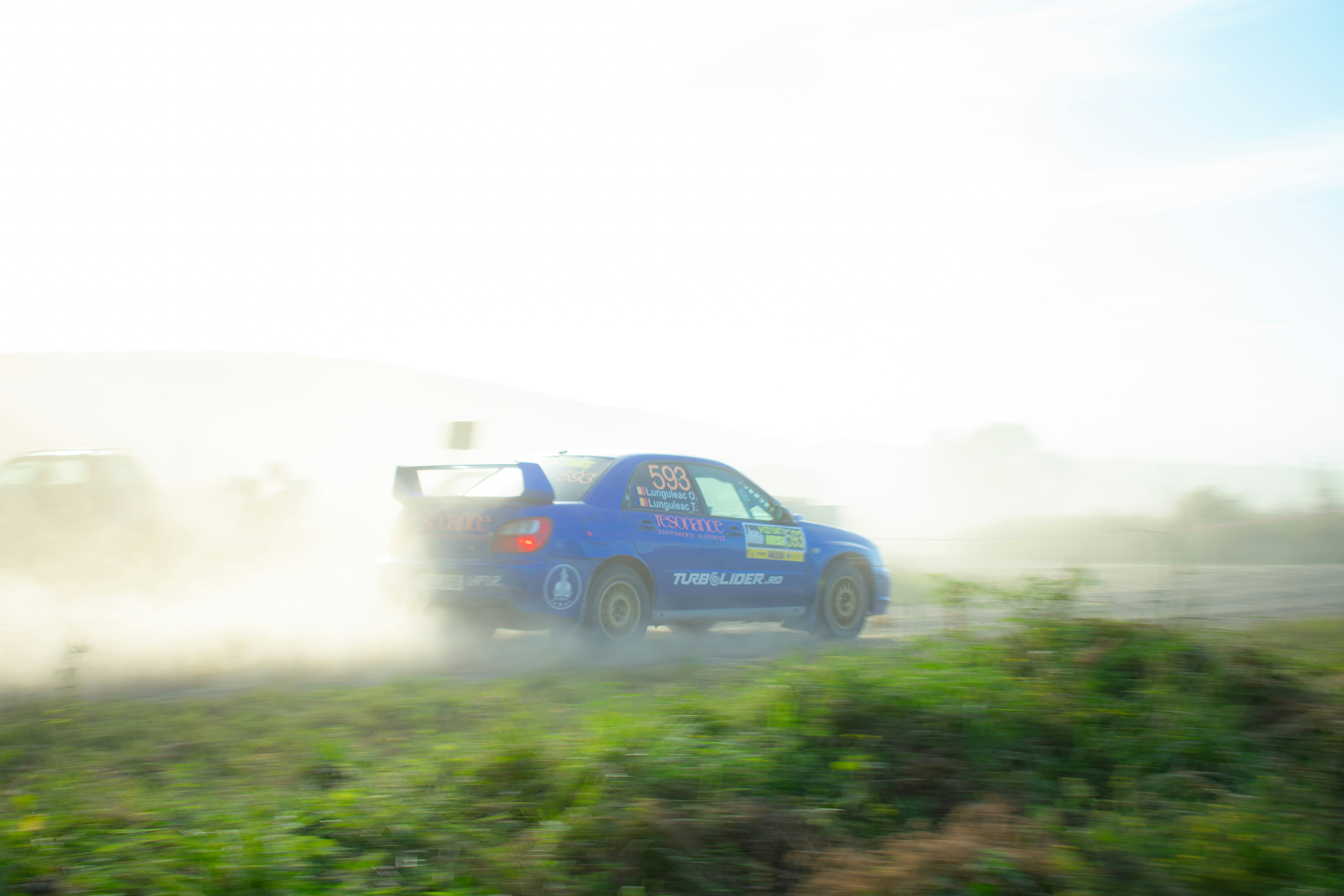 Dust Trail Dynamo: Blue Rally Car Surging Across Sunlit Dirt