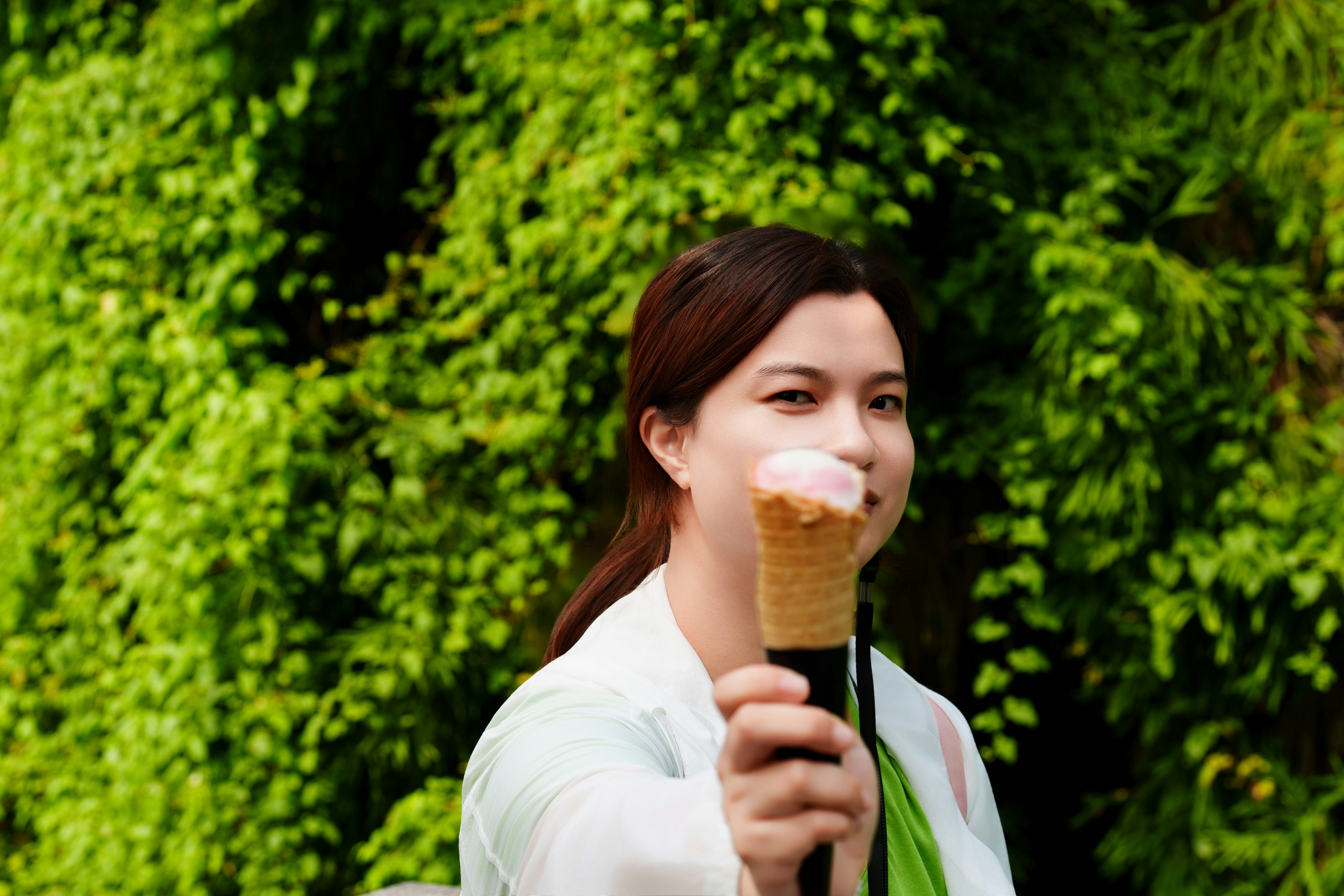 Woman holding an ice cream cone in front of greenery