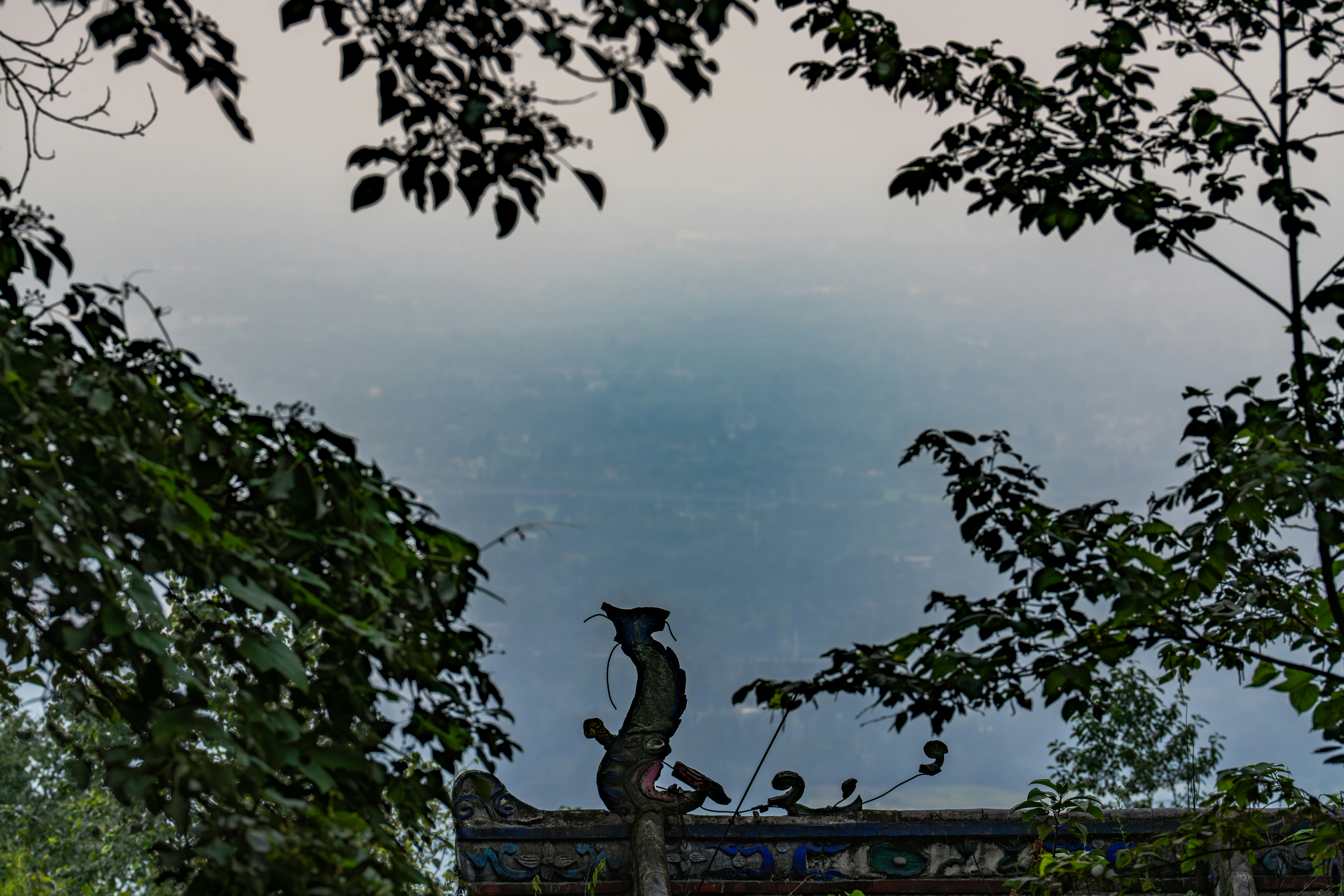 Dragon sculpture on a rooftop seen through trees.