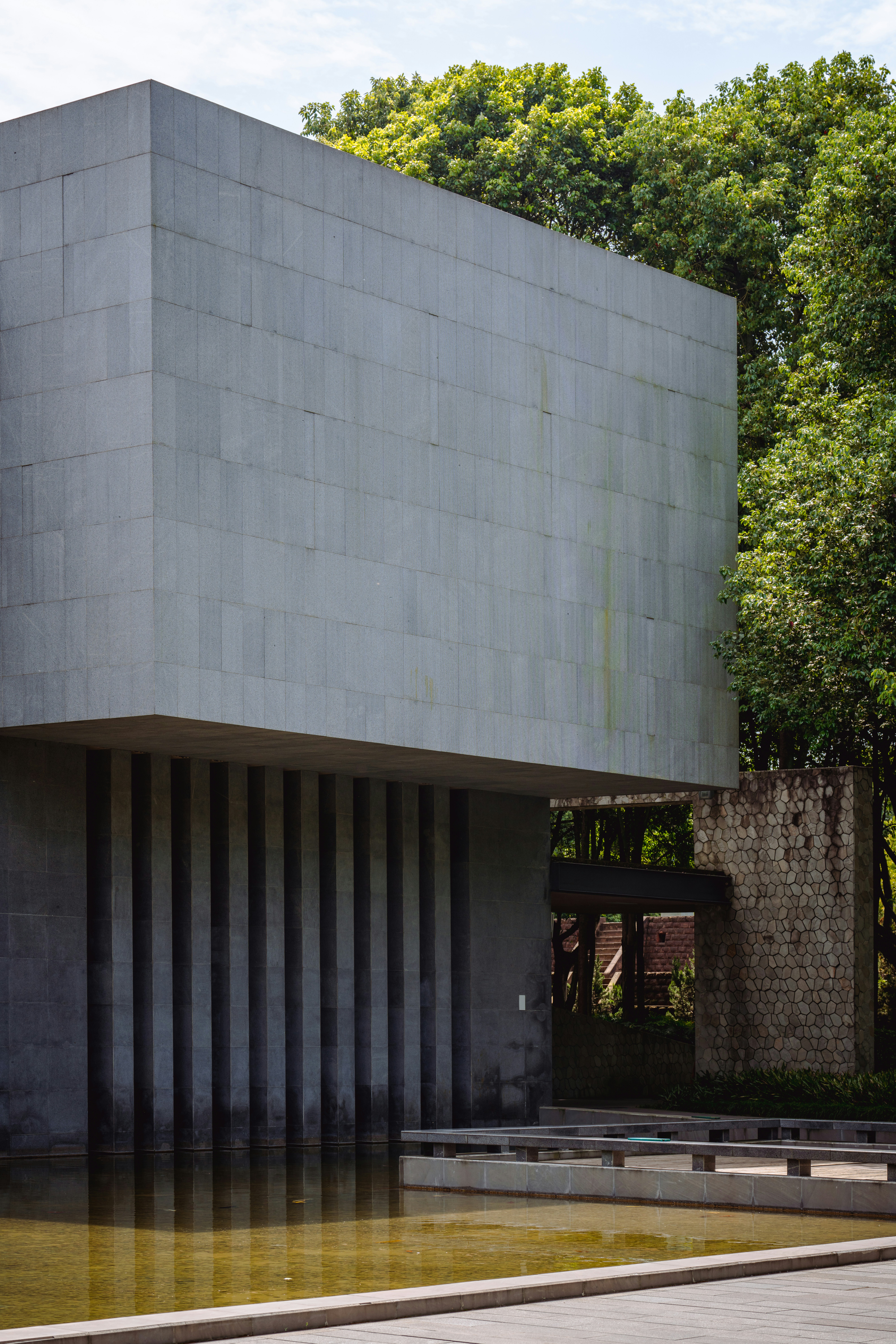 Modern concrete building with reflecting pool and trees.