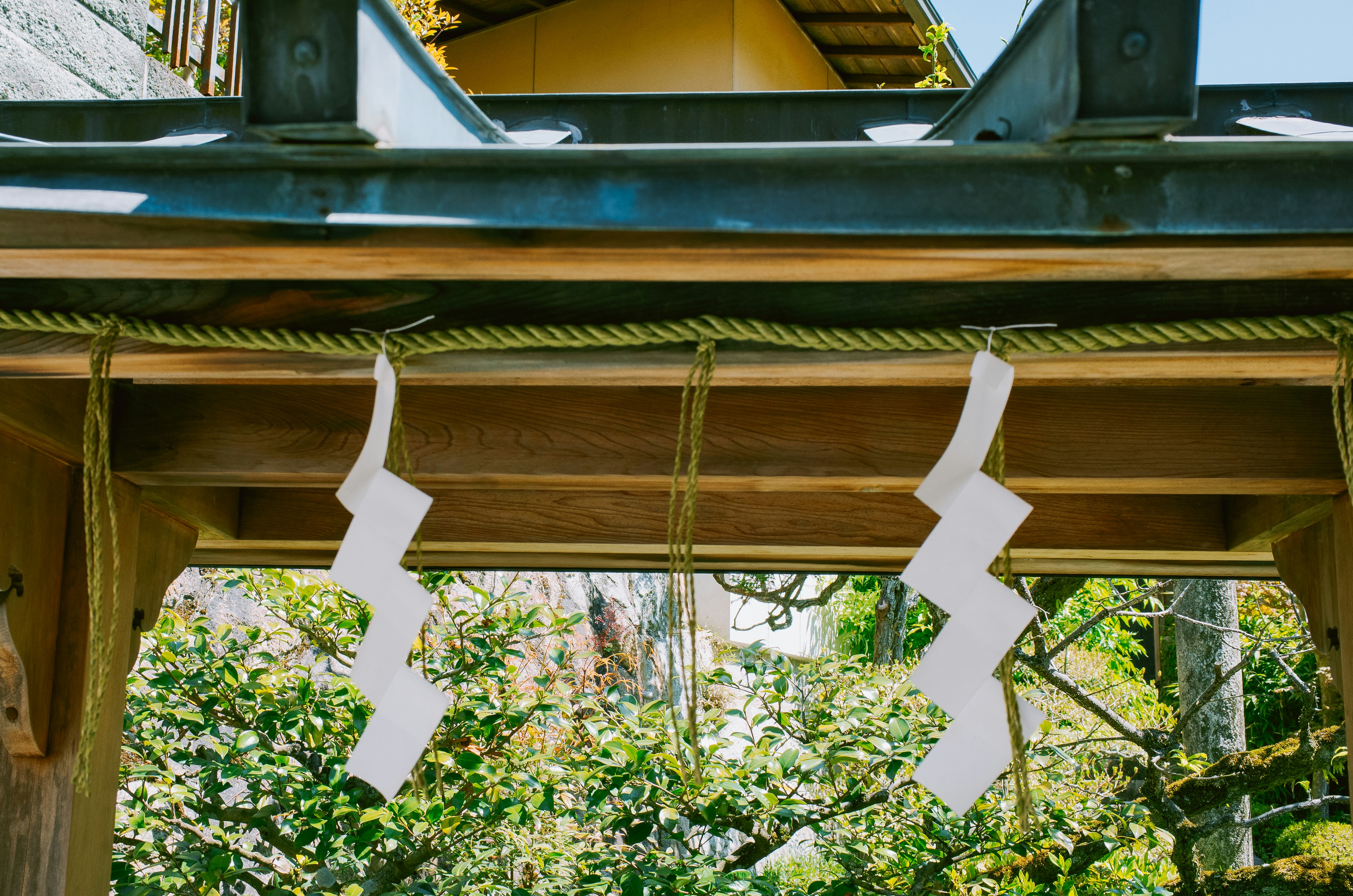 Two white paper shimenawa hang from wooden beams.
