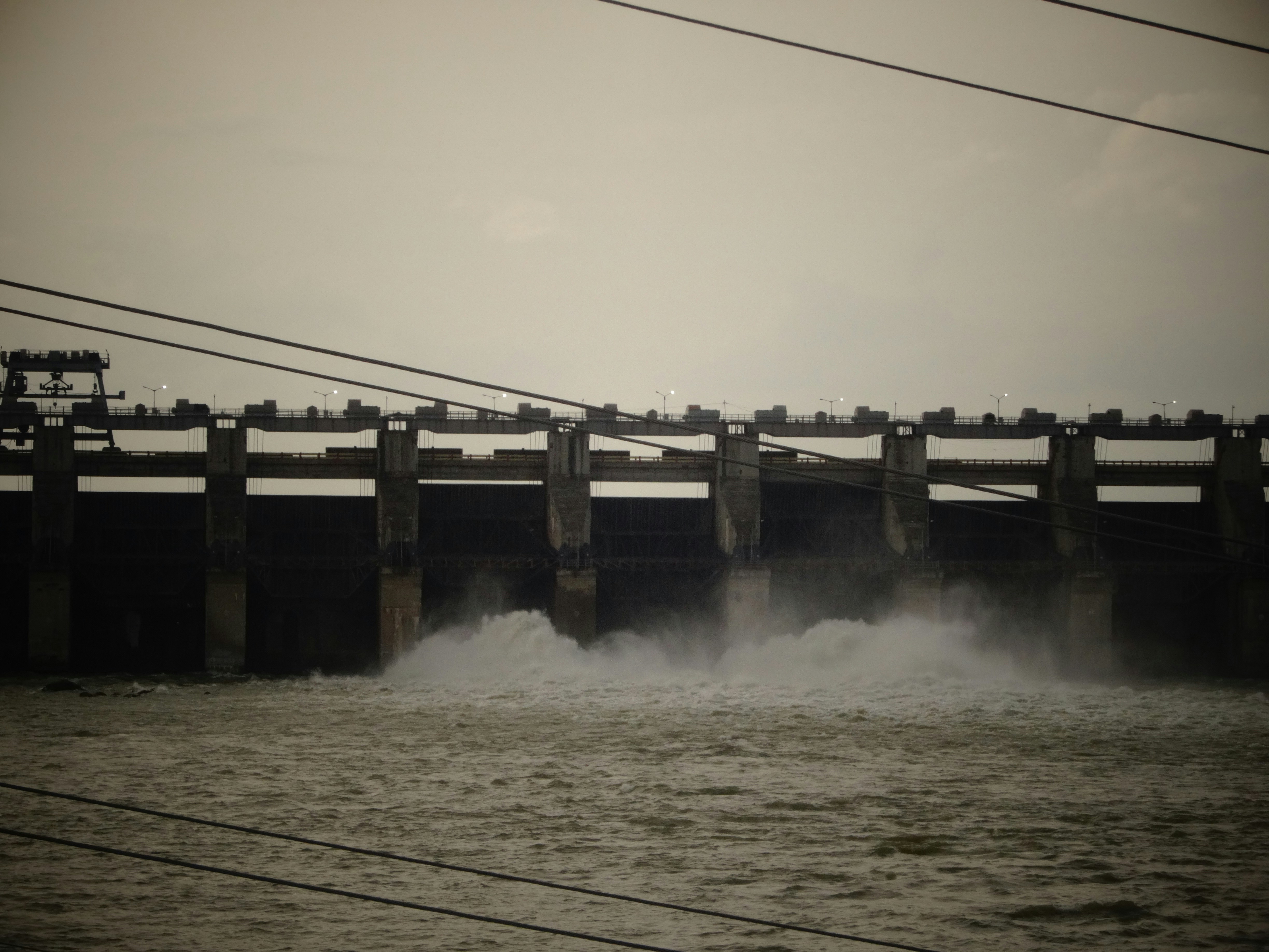Hydroelectric dam releasing water into the river, surrounded by a moody sky and power lines. The scene captures the dynamic interaction between technology and nature.