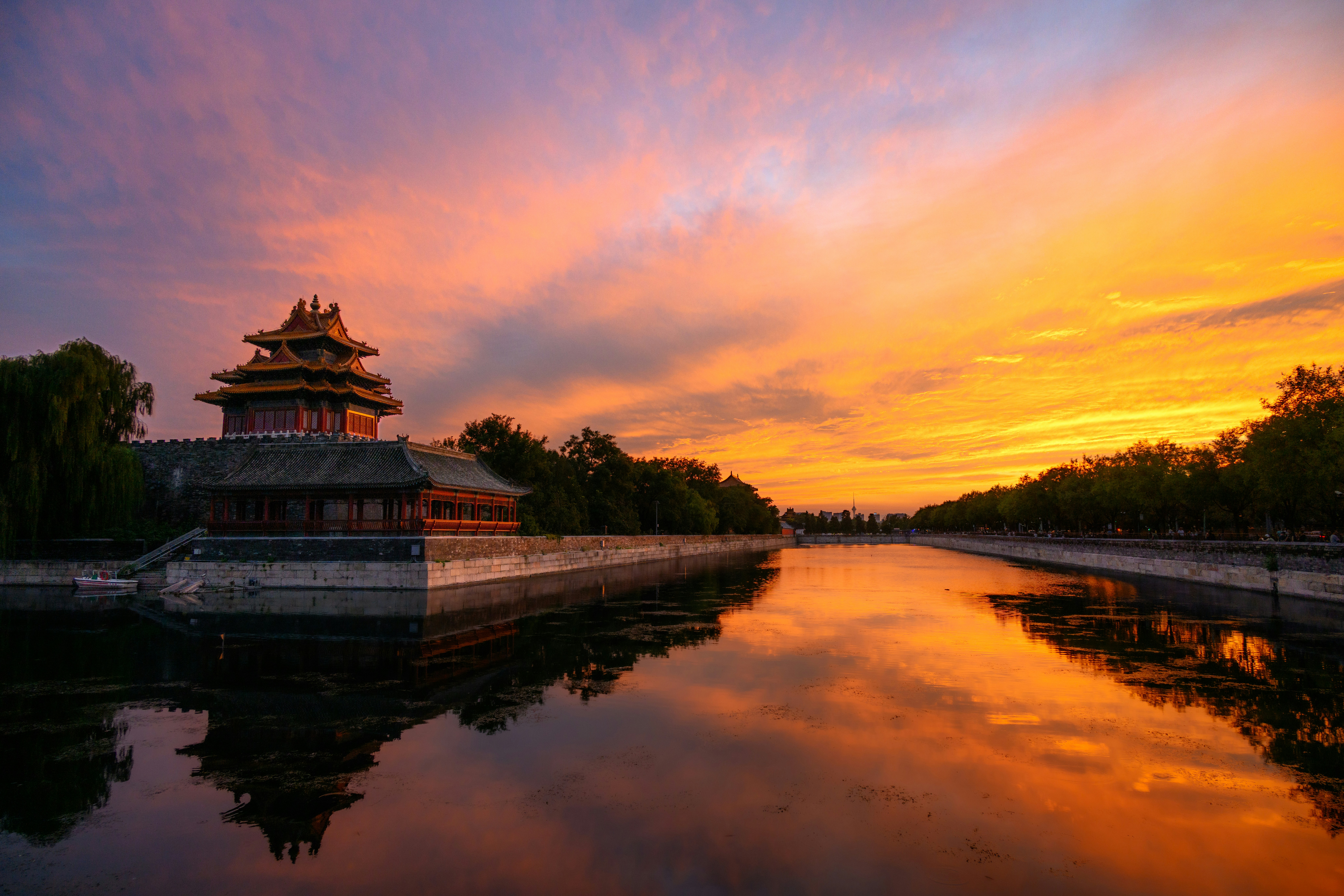 Traditional chinese architecture beside a calm river at sunset.