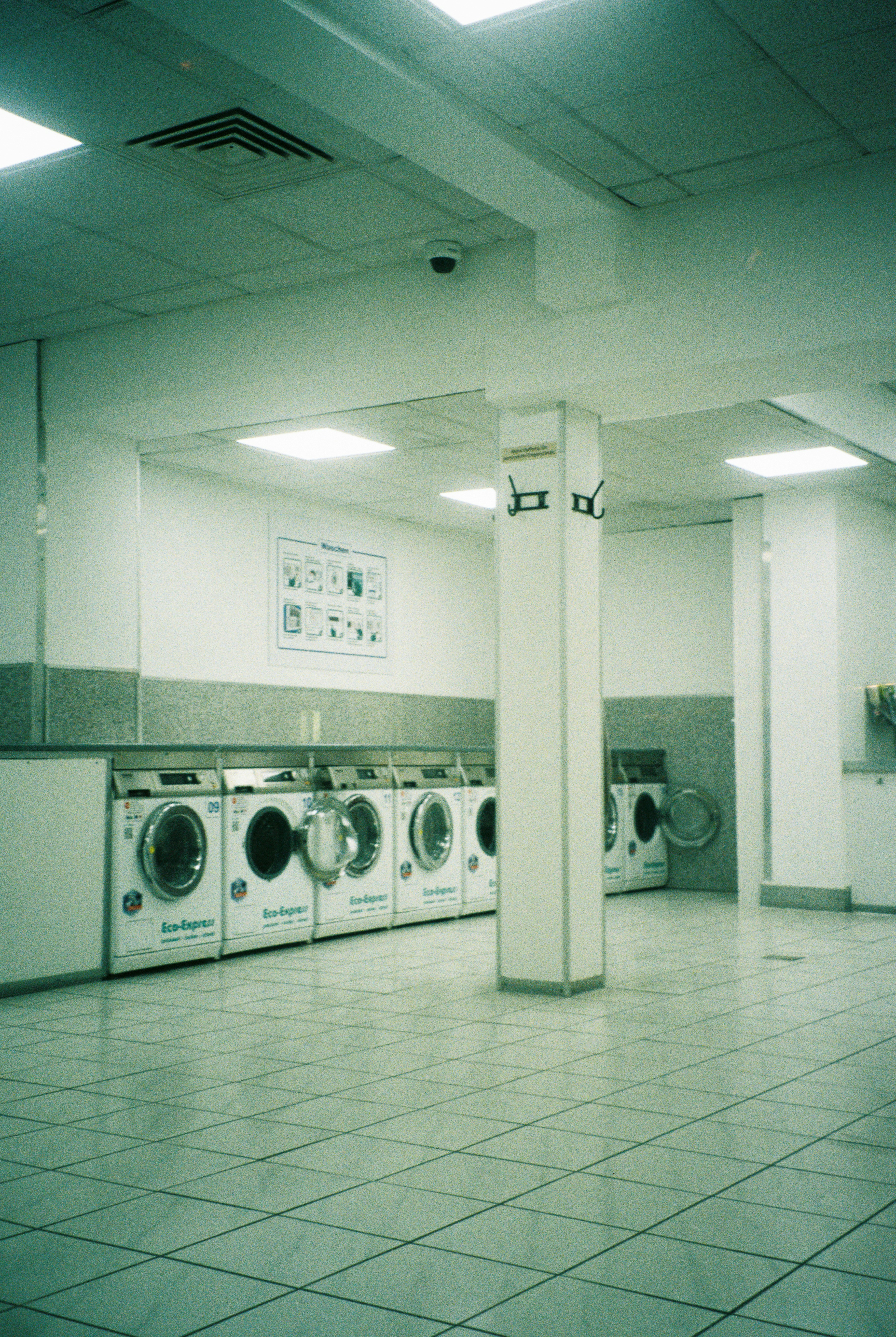 Shot on Kodak Gold 200 | Row of washing machines in a brightly lit laundromat.