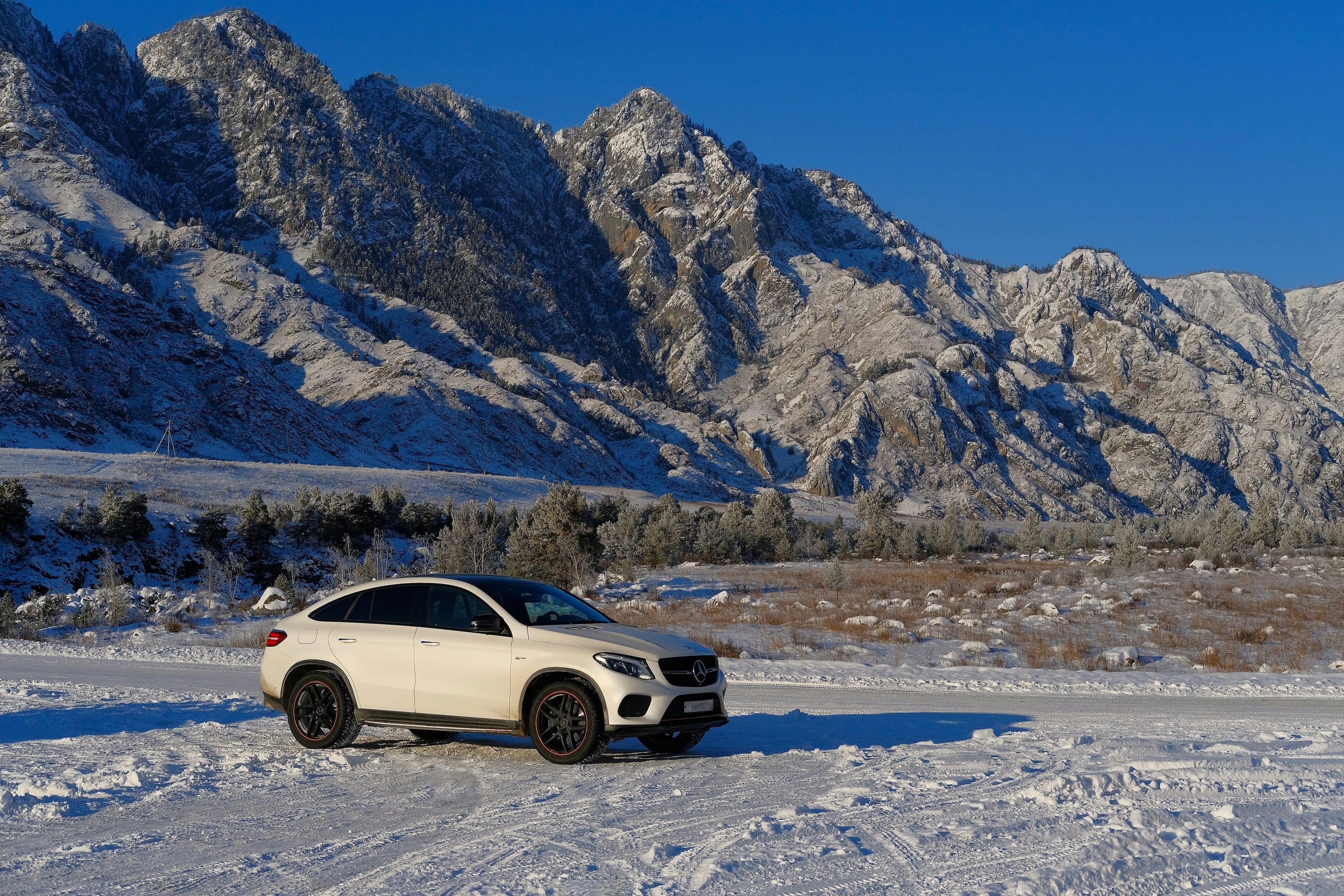 White suv parked on a snowy road with mountains.