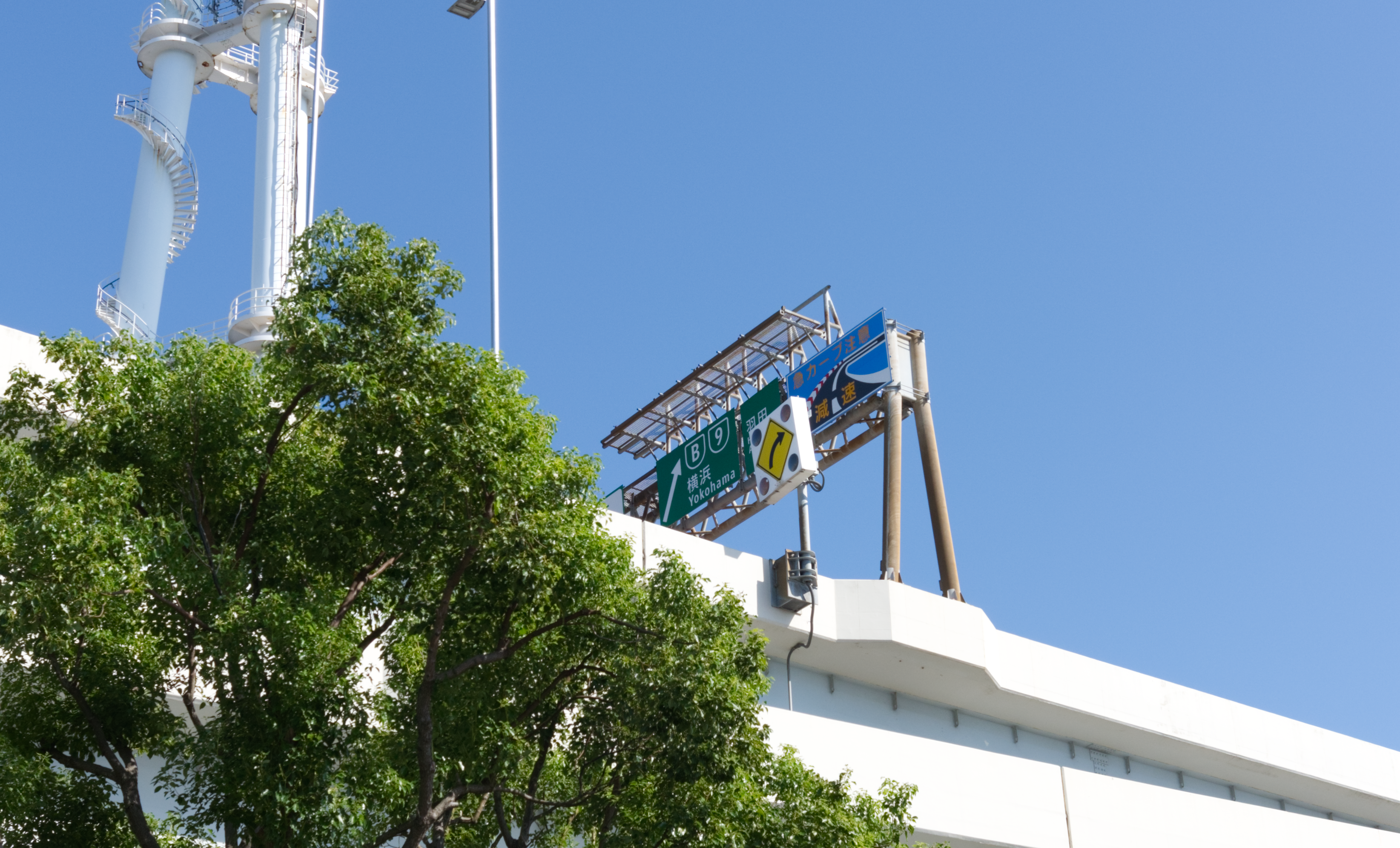 White elevated highway structure with green trees and blue sky.