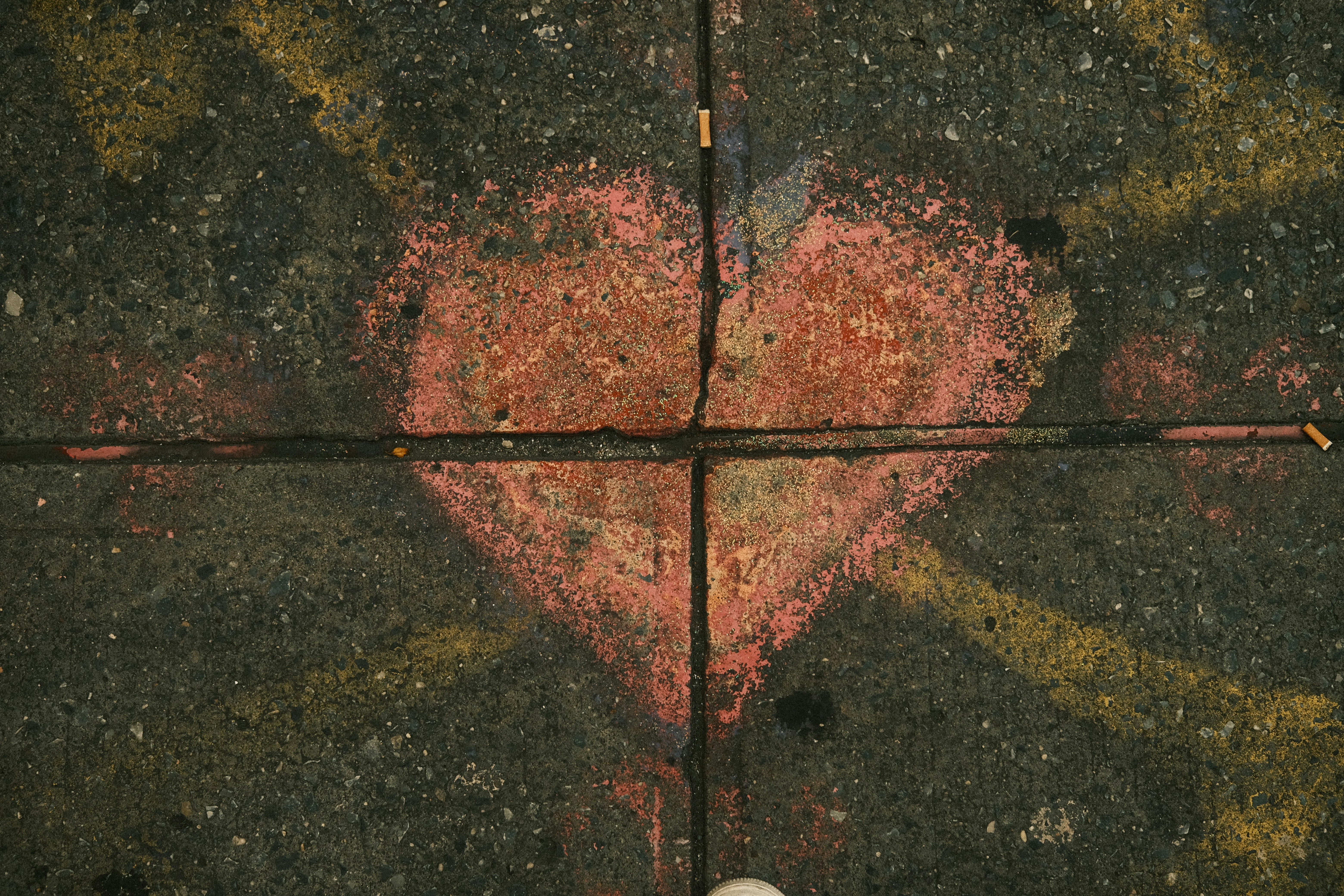 Colorful chalk heart drawn on a concrete sidewalk, surrounded by vibrant patterns and scattered cigarette butts.