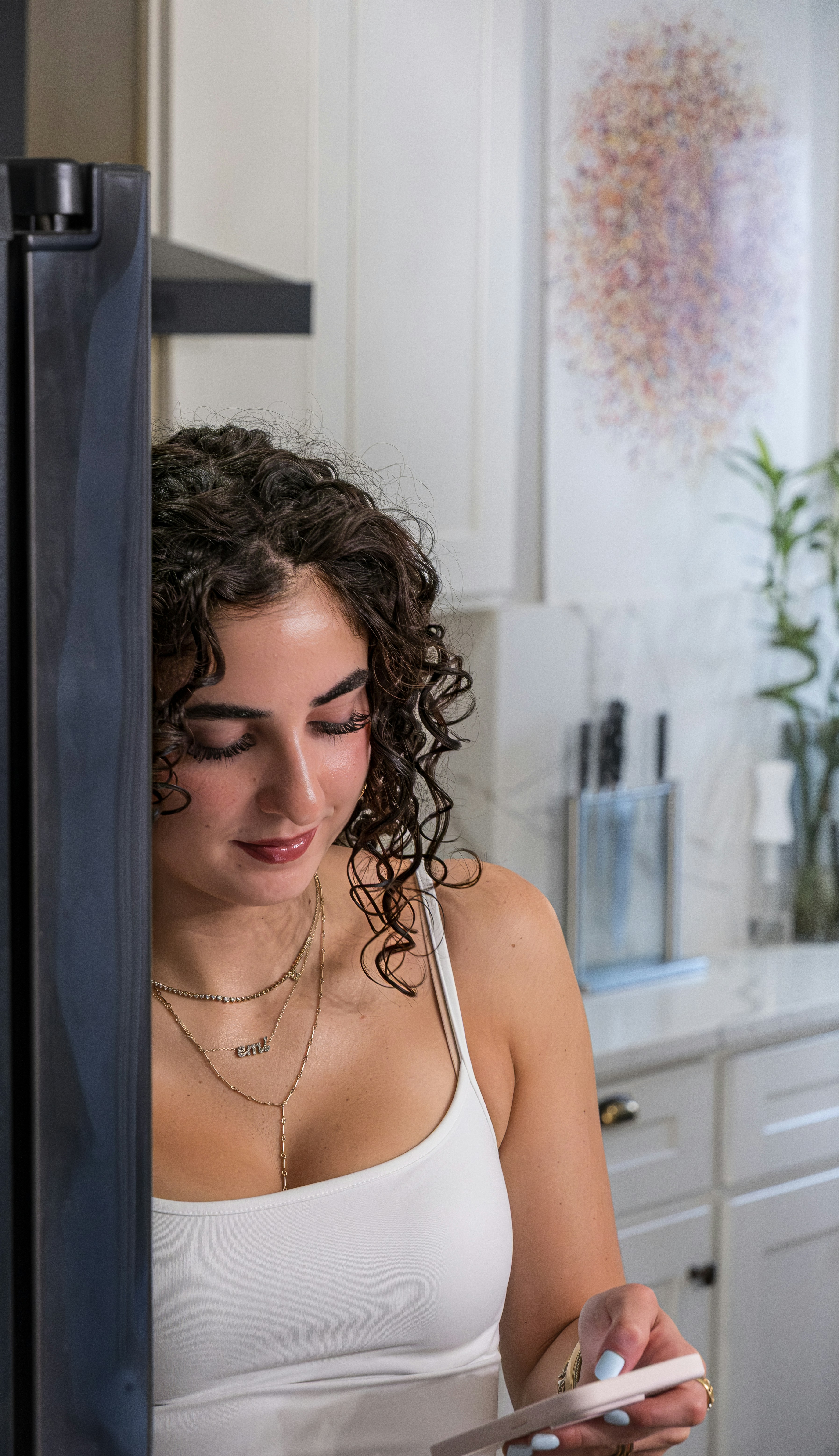 Young woman looking at phone with kitchen in background | A woman looking at her phone in a kitchen.