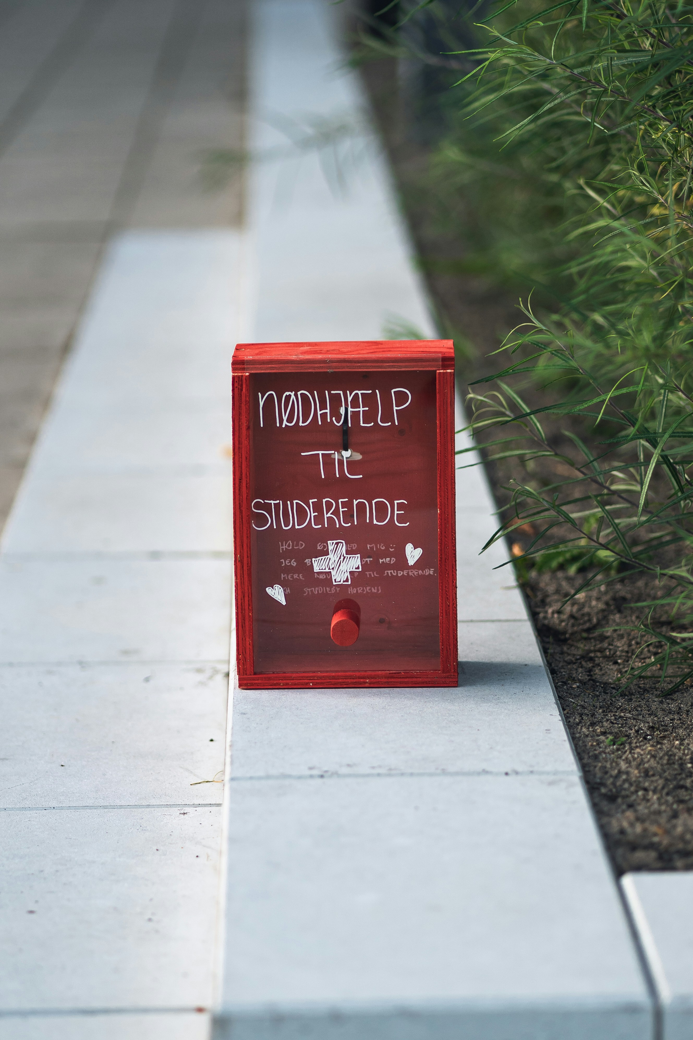 Red emergency aid box for students on a sidewalk.