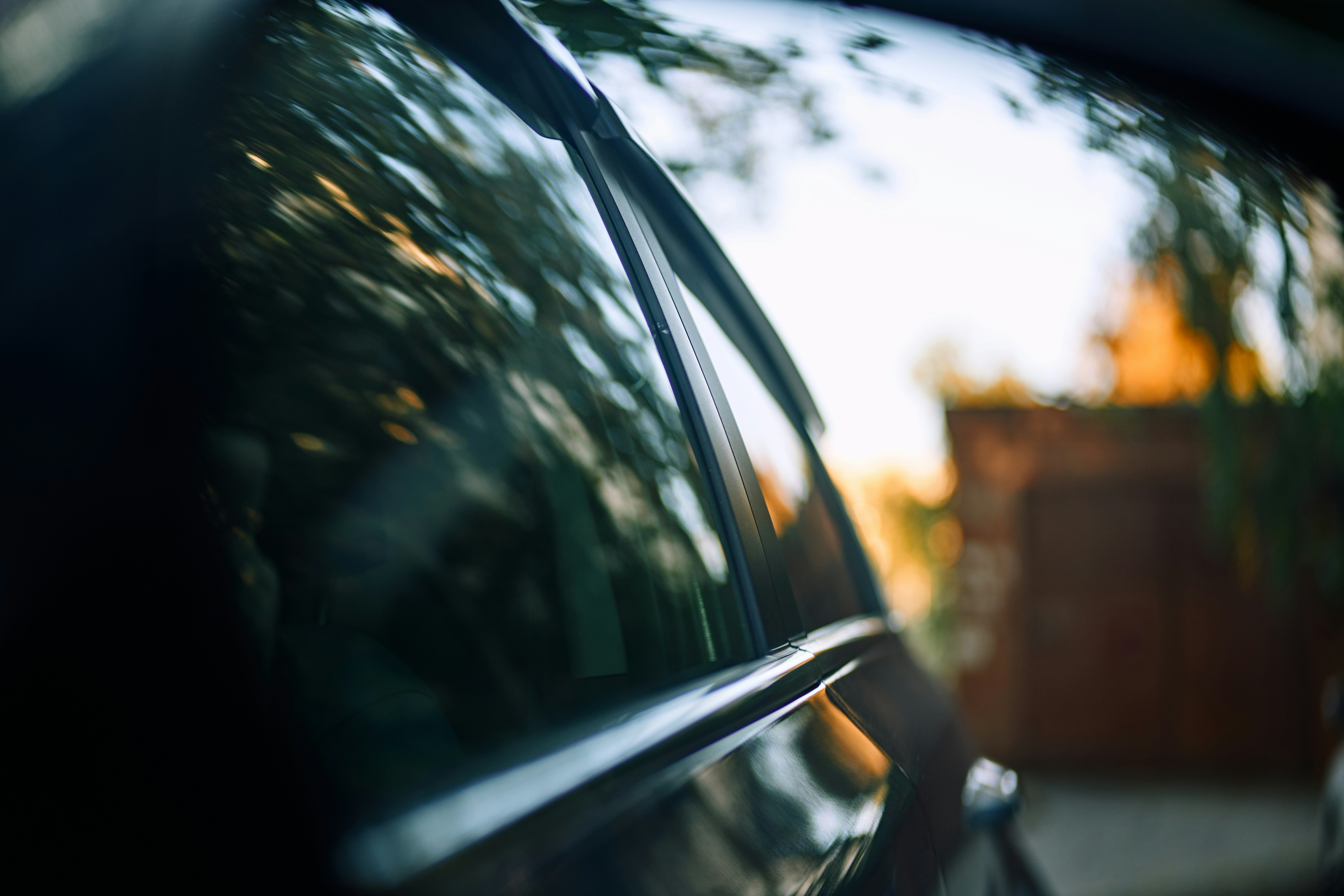 A soft-focus view of a car's side mirror reflecting a warm, sunset-lit background with hints of greenery.