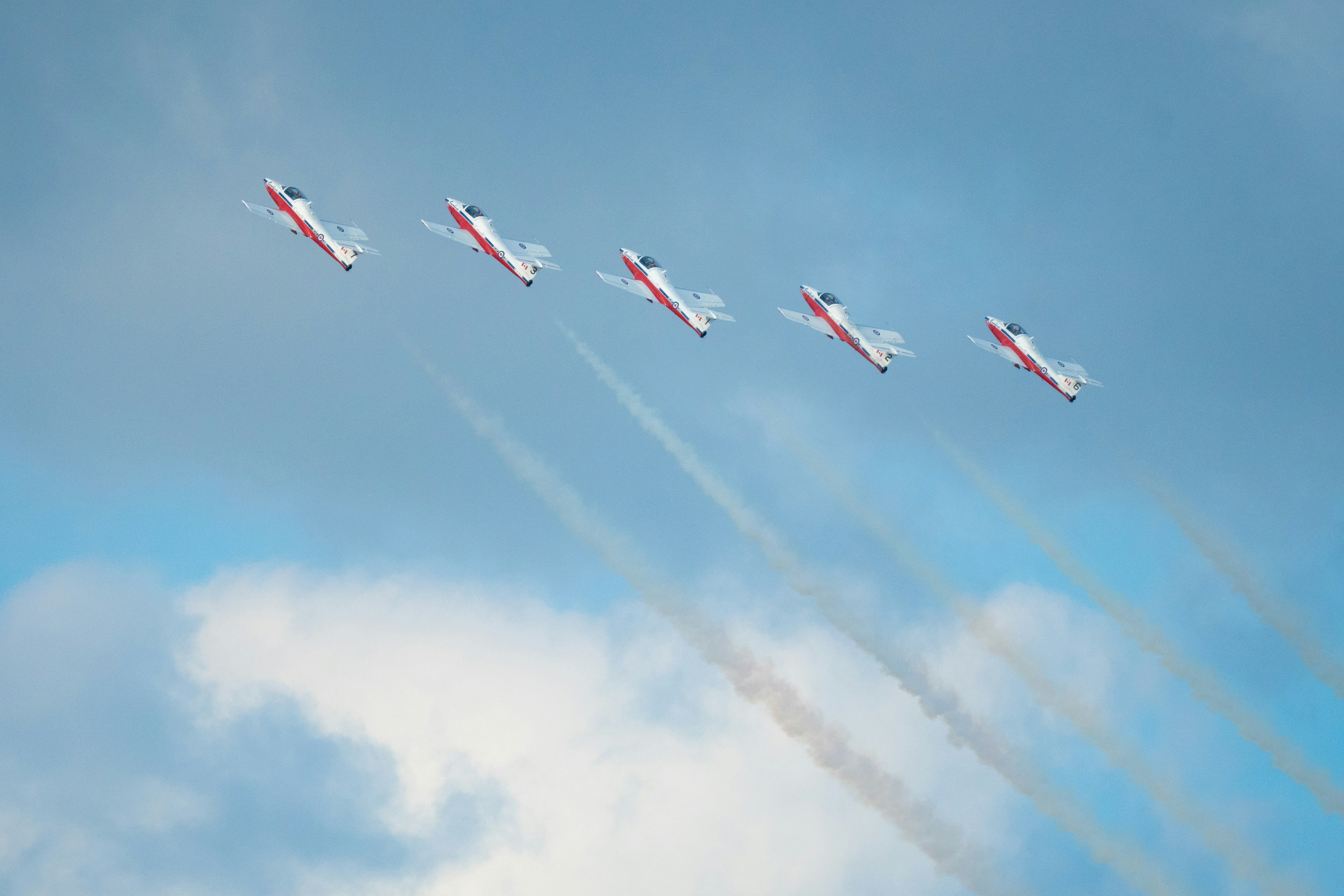 Five aircraft executing a synchronized formation in a clear blue sky, leaving trails of smoke behind them.