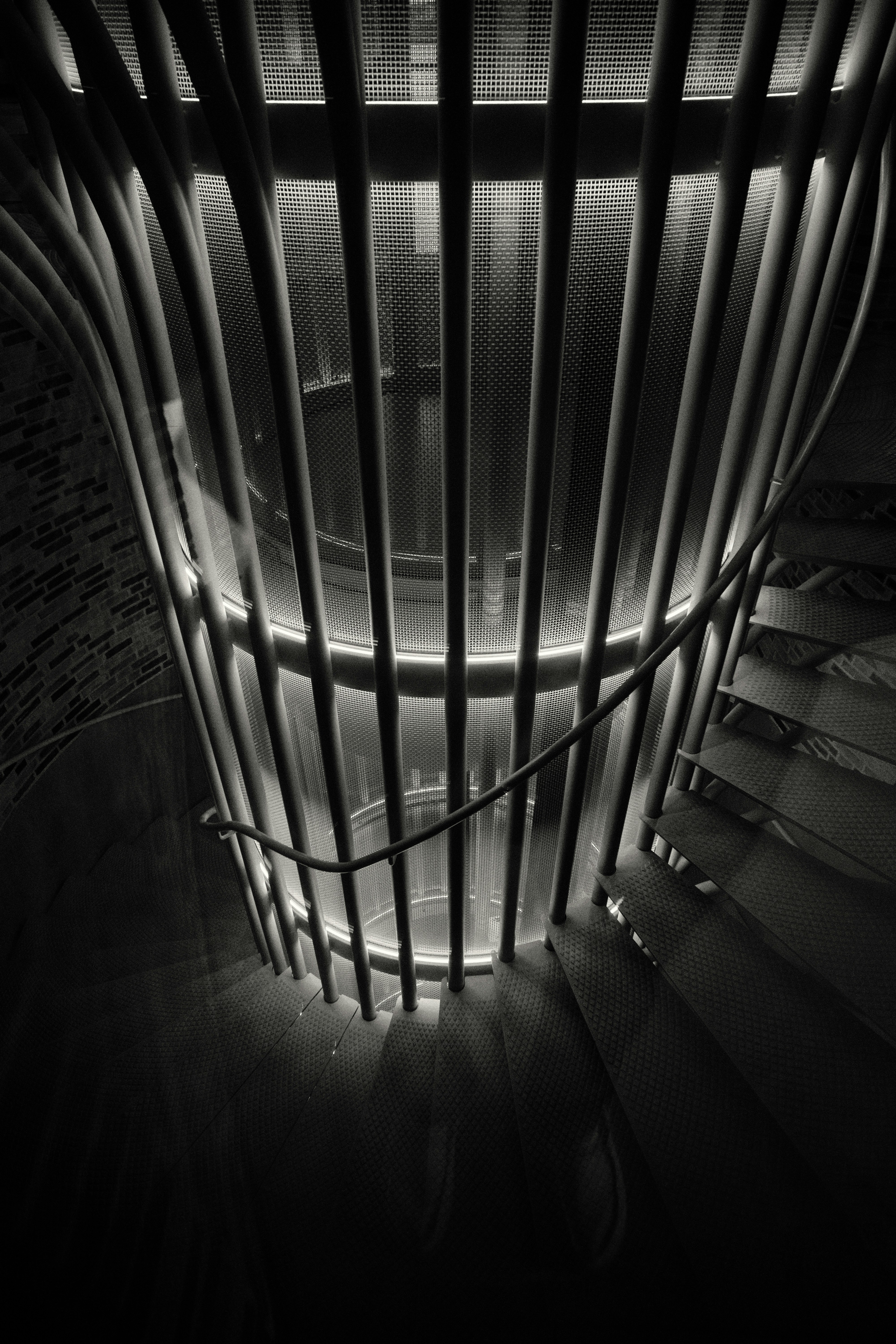 Interior staircase detail of Fjordenhus in Vejle, Denmark. Black and white shot highlighting curves, light reflections, and the building’s sculptural geometry. | Modern spiral staircase with dramatic lighting