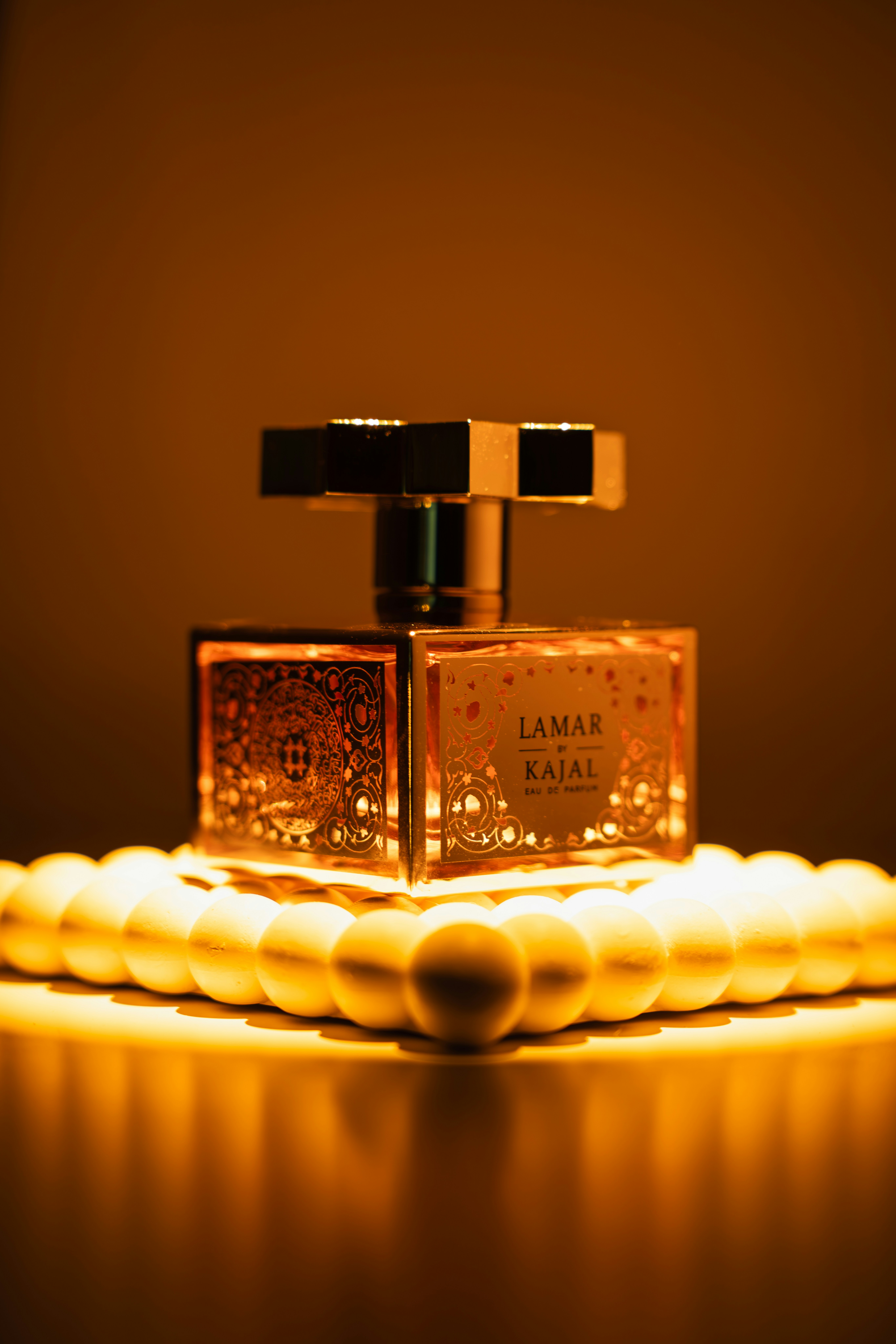 A luxurious perfume bottle elegantly displayed on a circular arrangement of white spheres, illuminated by a warm golden glow.