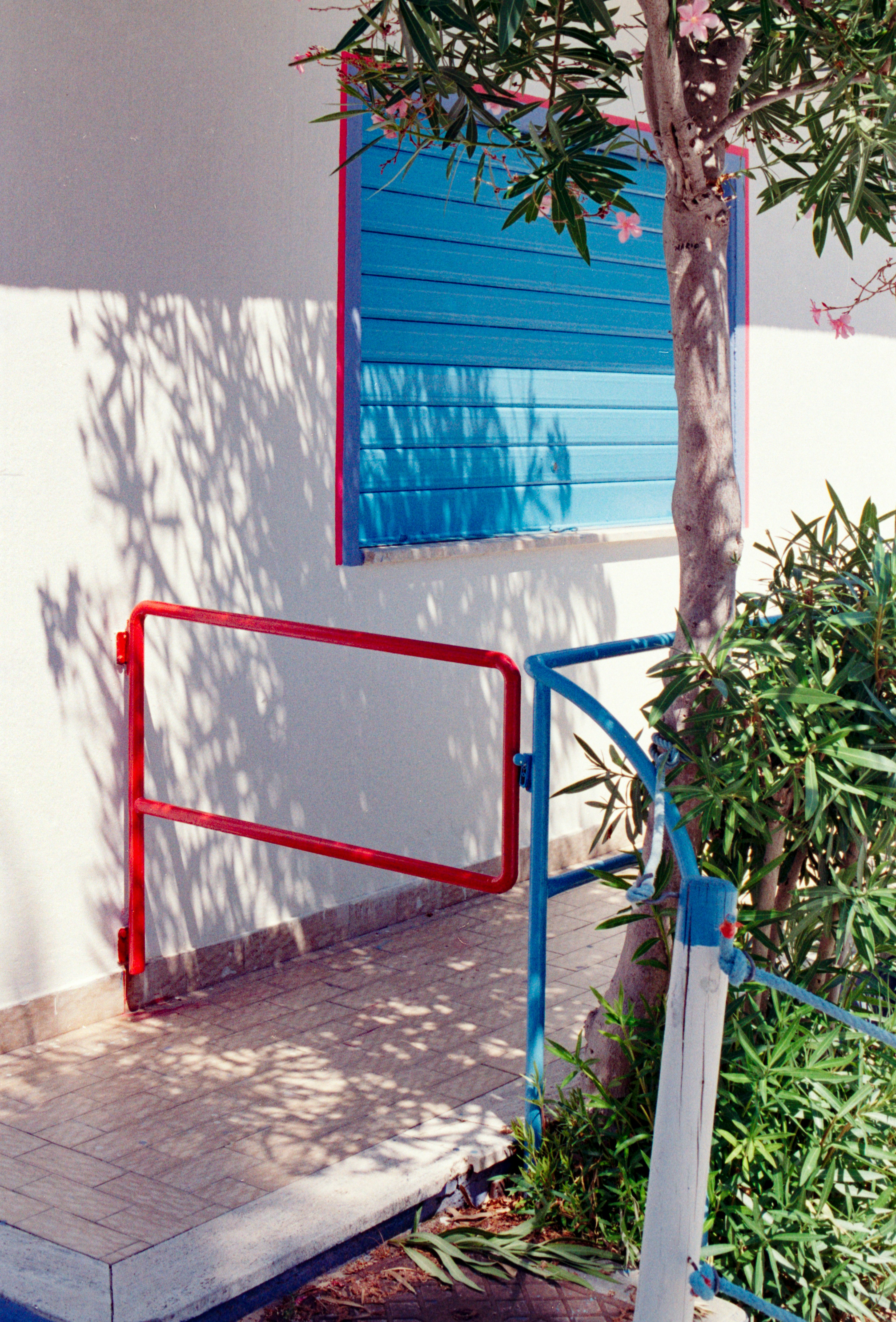 A white wall with blue shutters and red railing.