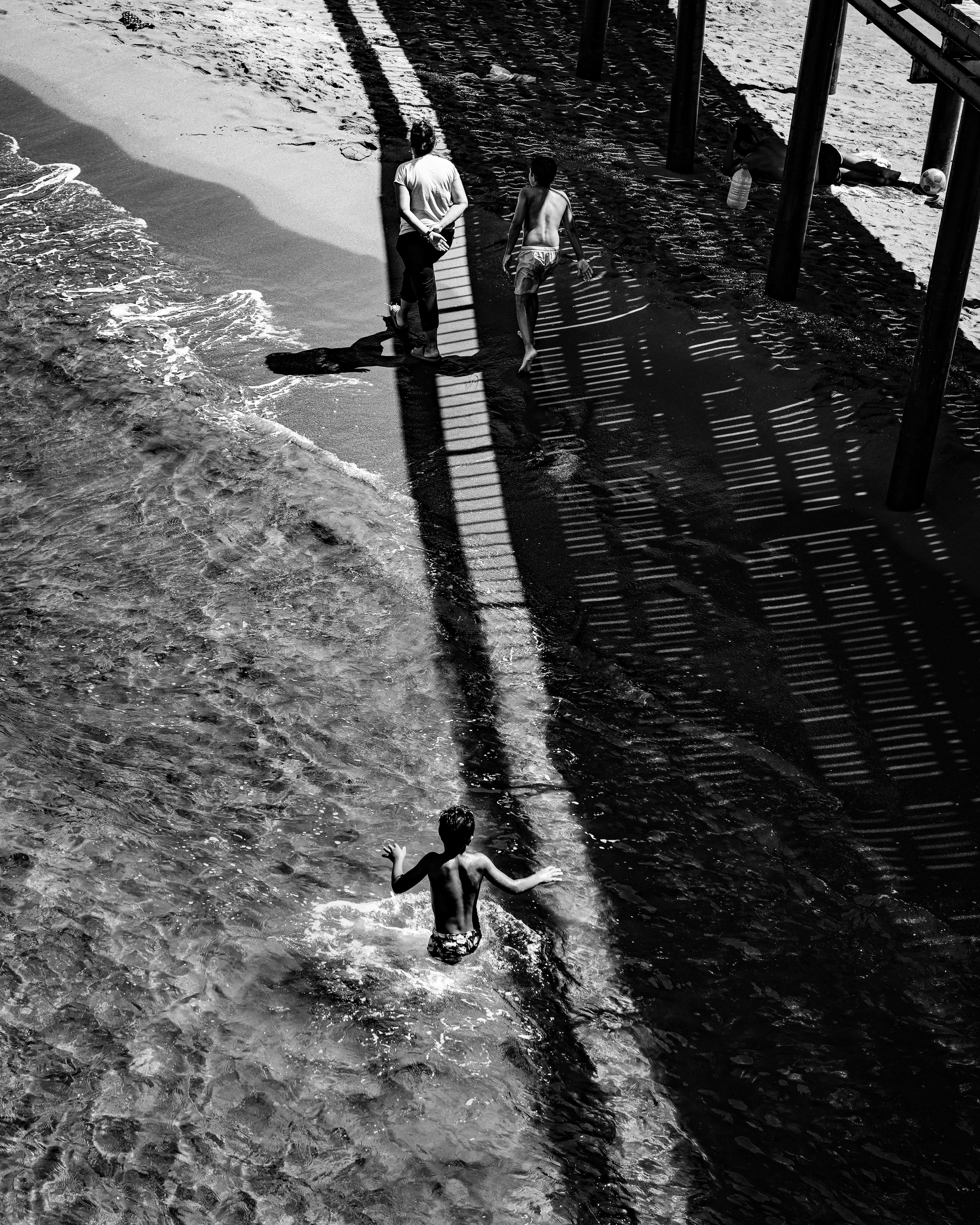 Summer day | Children playing in the ocean near a wooden pier.