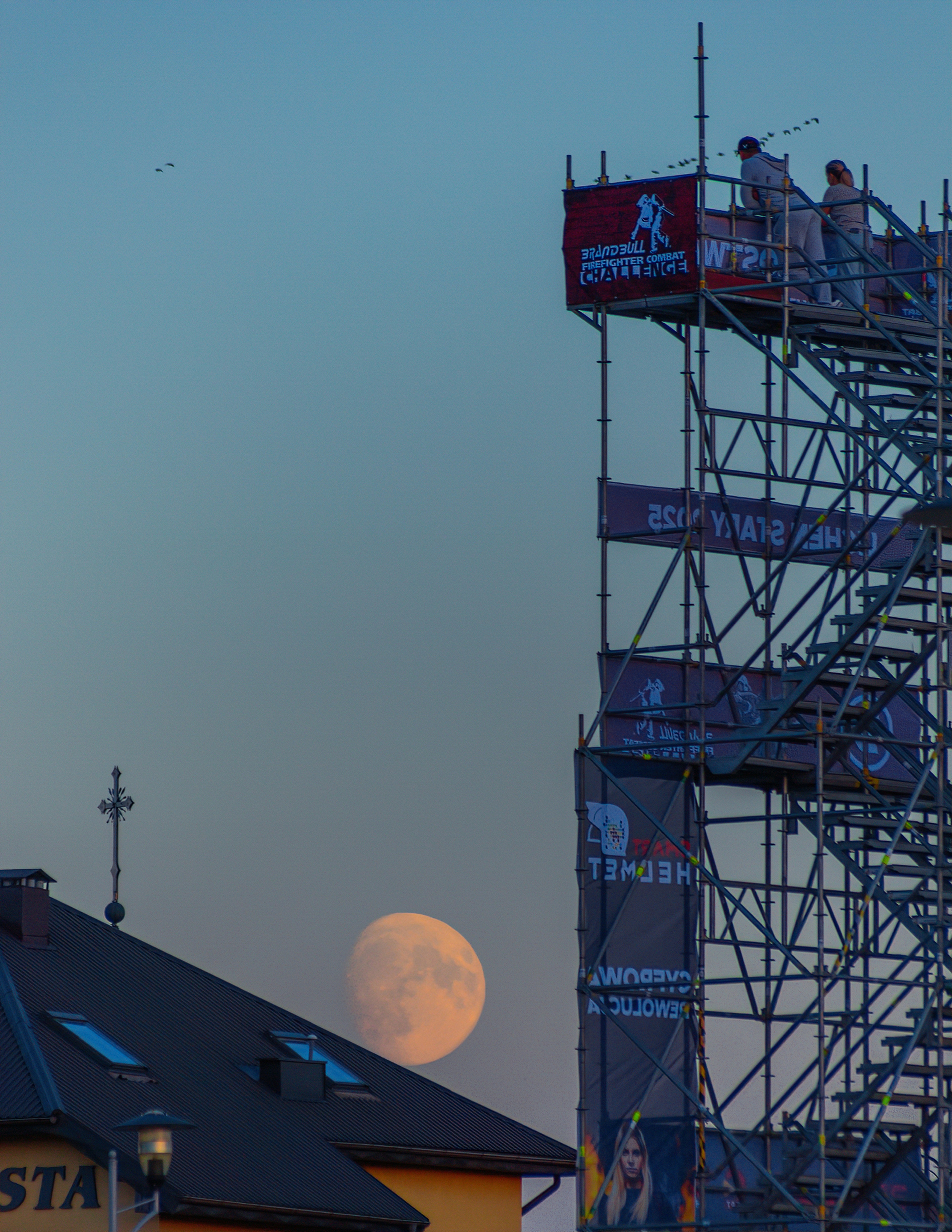 Full moon rises behind scaffolding and building.