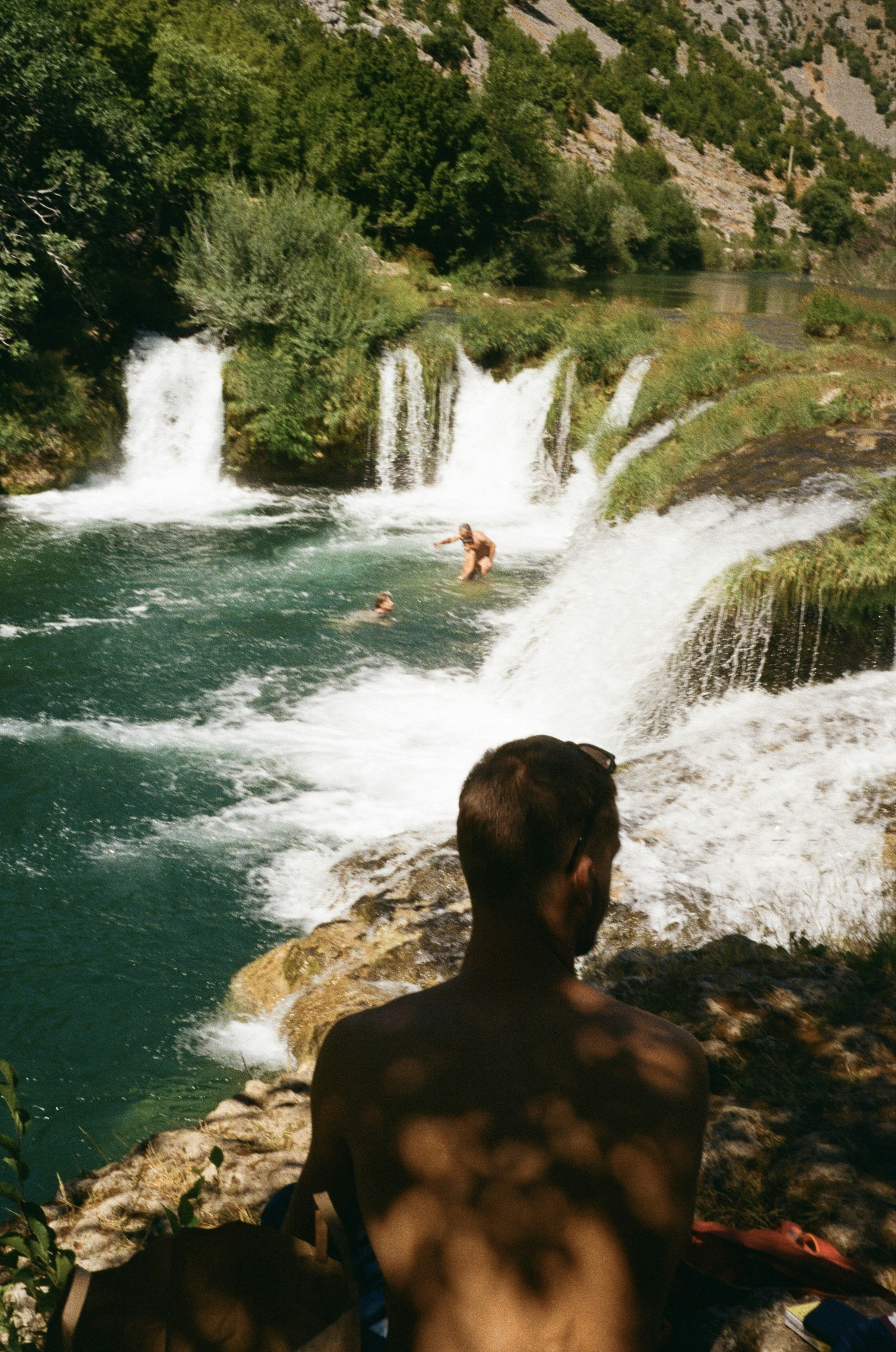 People swimming in waterfalls surrounded by lush greenery.