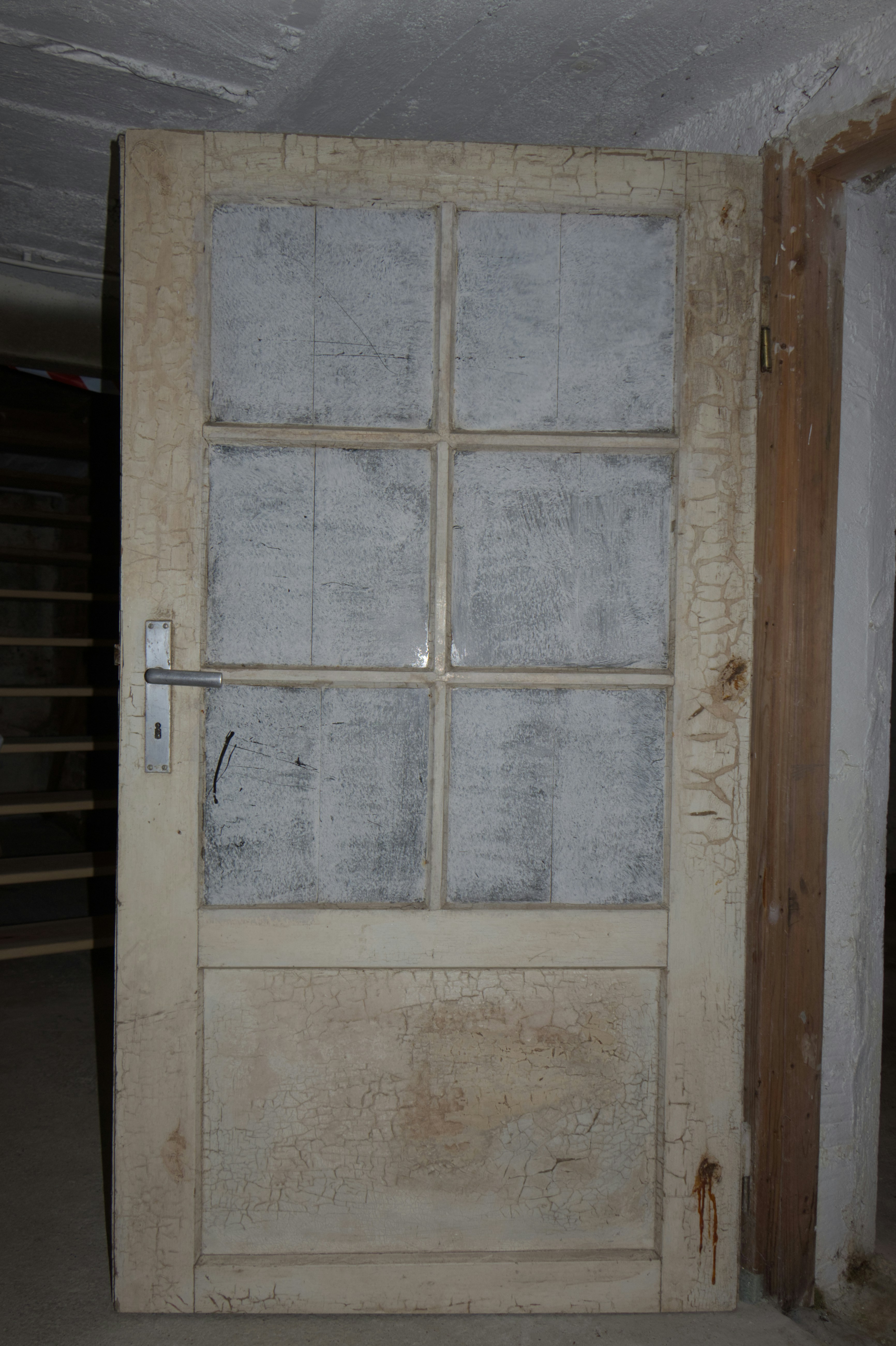 Weathered wooden door with cracked paint and glass panes, leading into an unknown space.