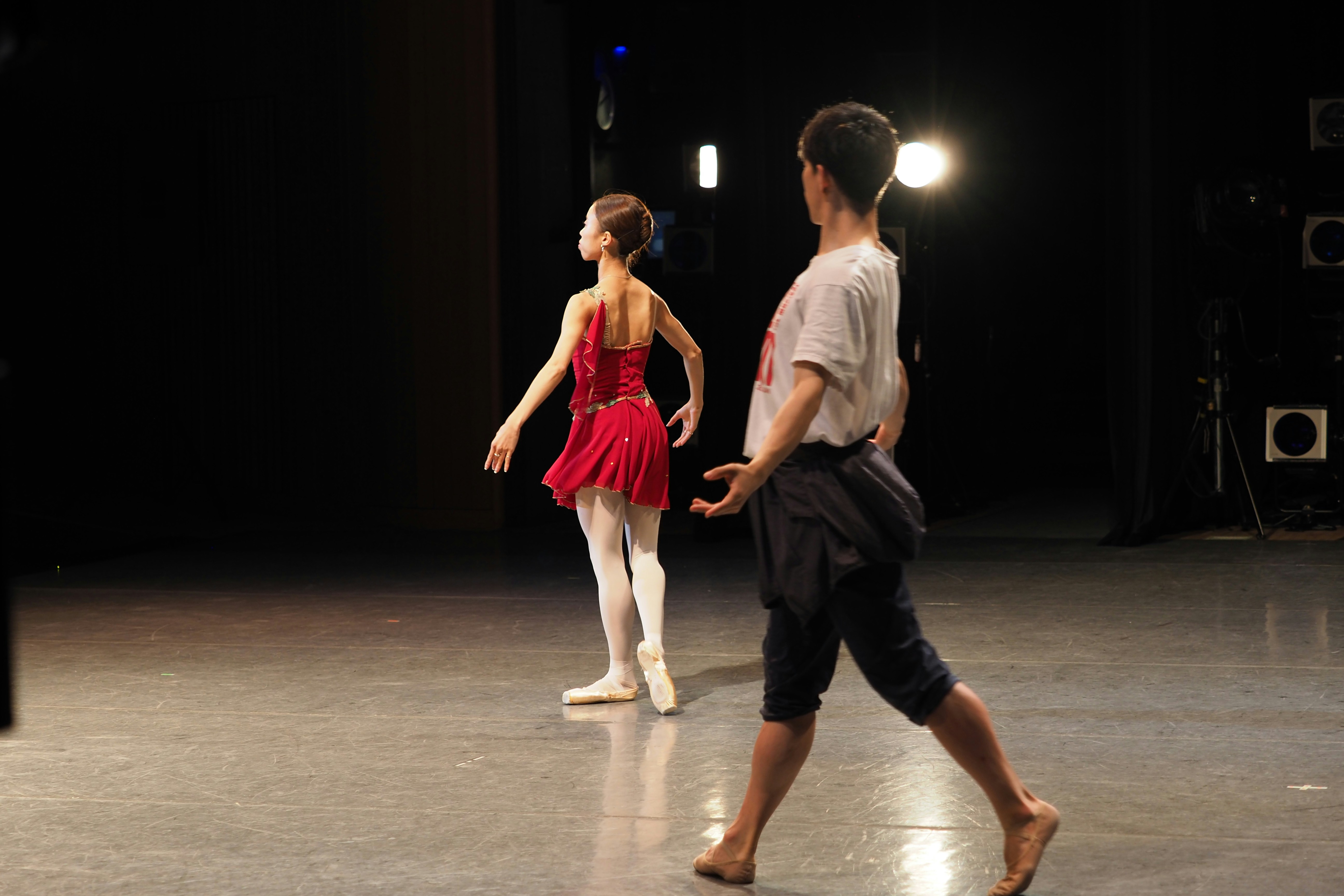 Two ballet dancers rehearsing on stage, showcasing their form and technique under soft stage lighting.