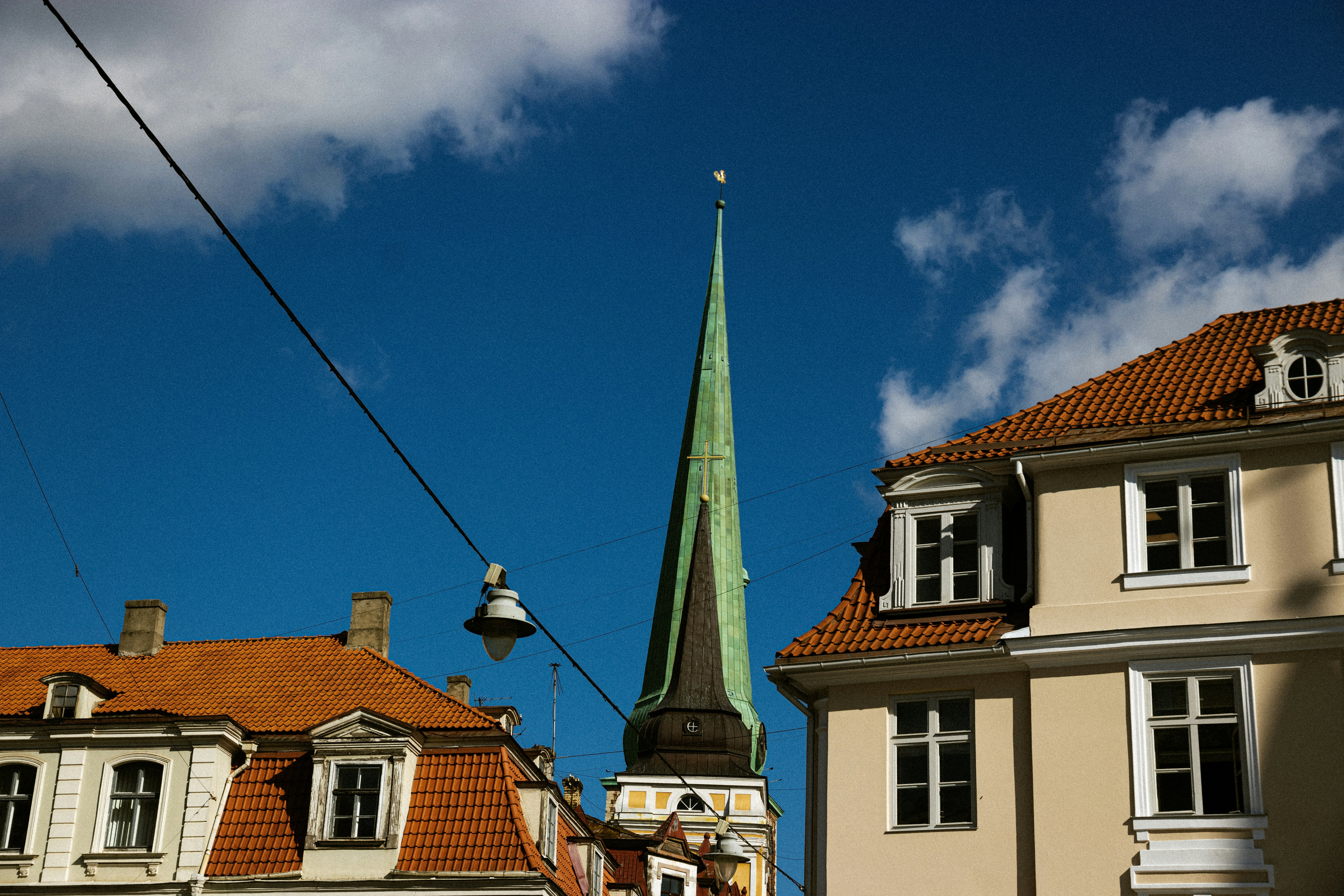 Green church steeple between old buildings under blue sky