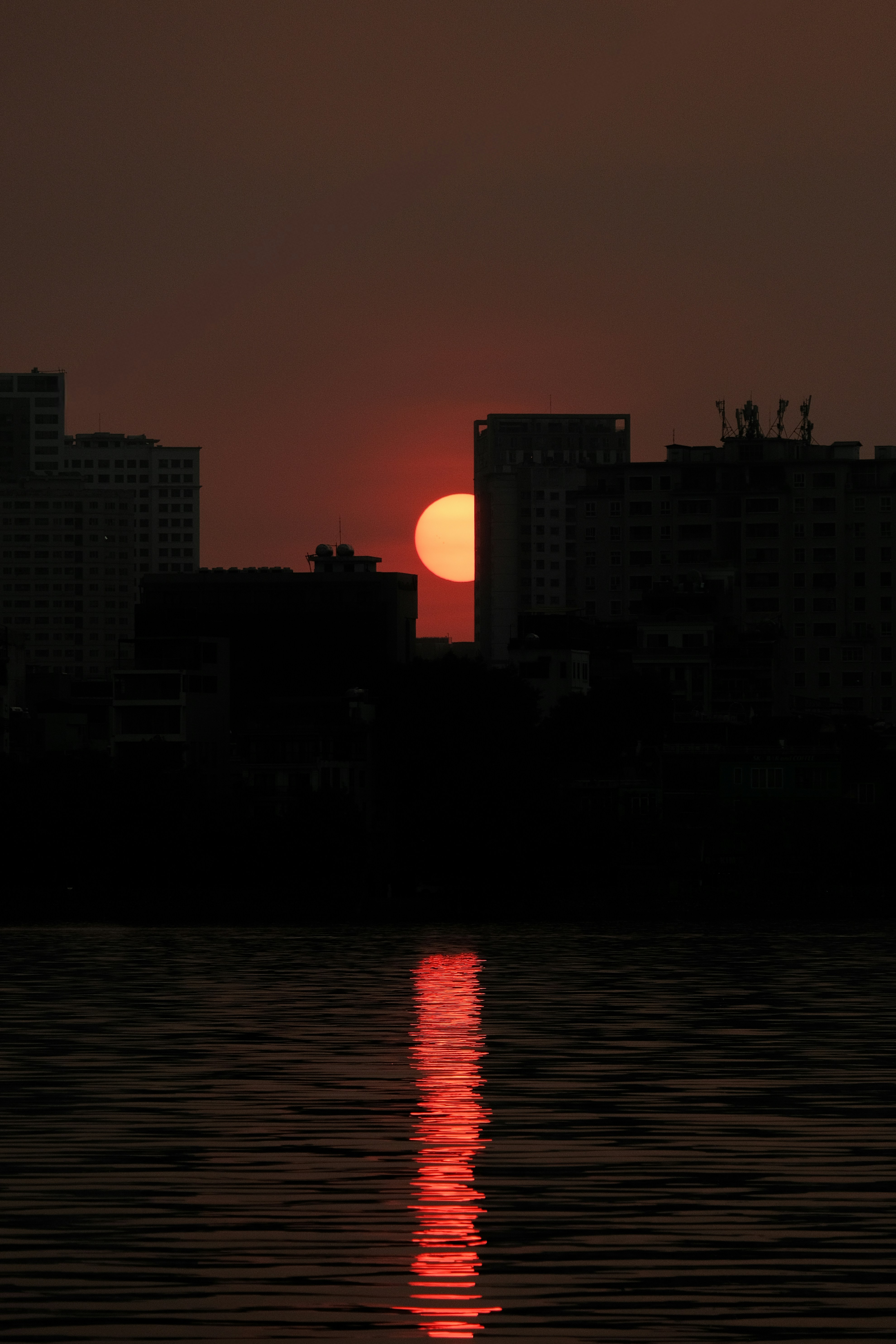 Sunset behind city buildings with water reflection