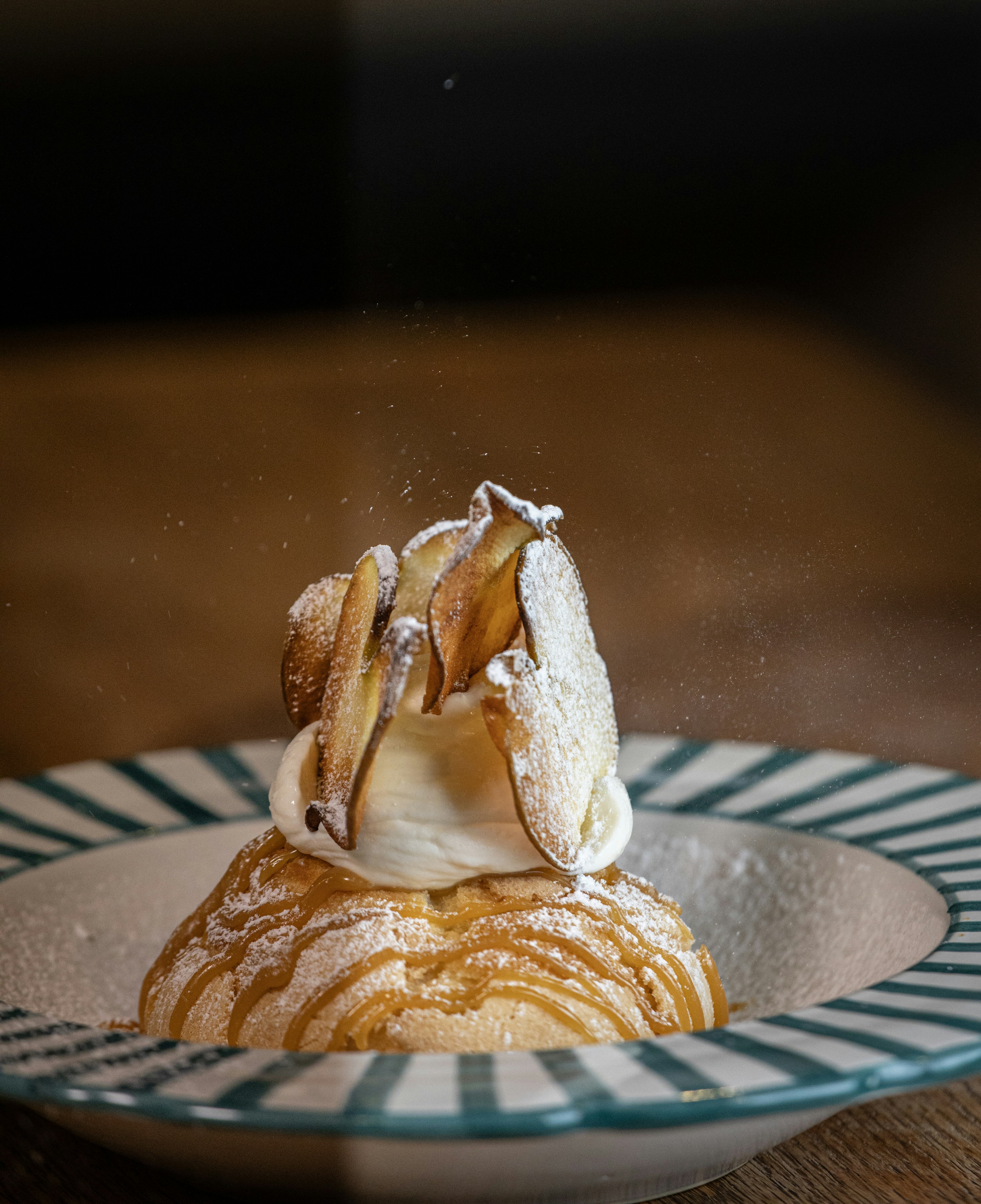 Delicate pastry topped with whipped cream and apple slices, dusted with powdered sugar, served on a striped plate.