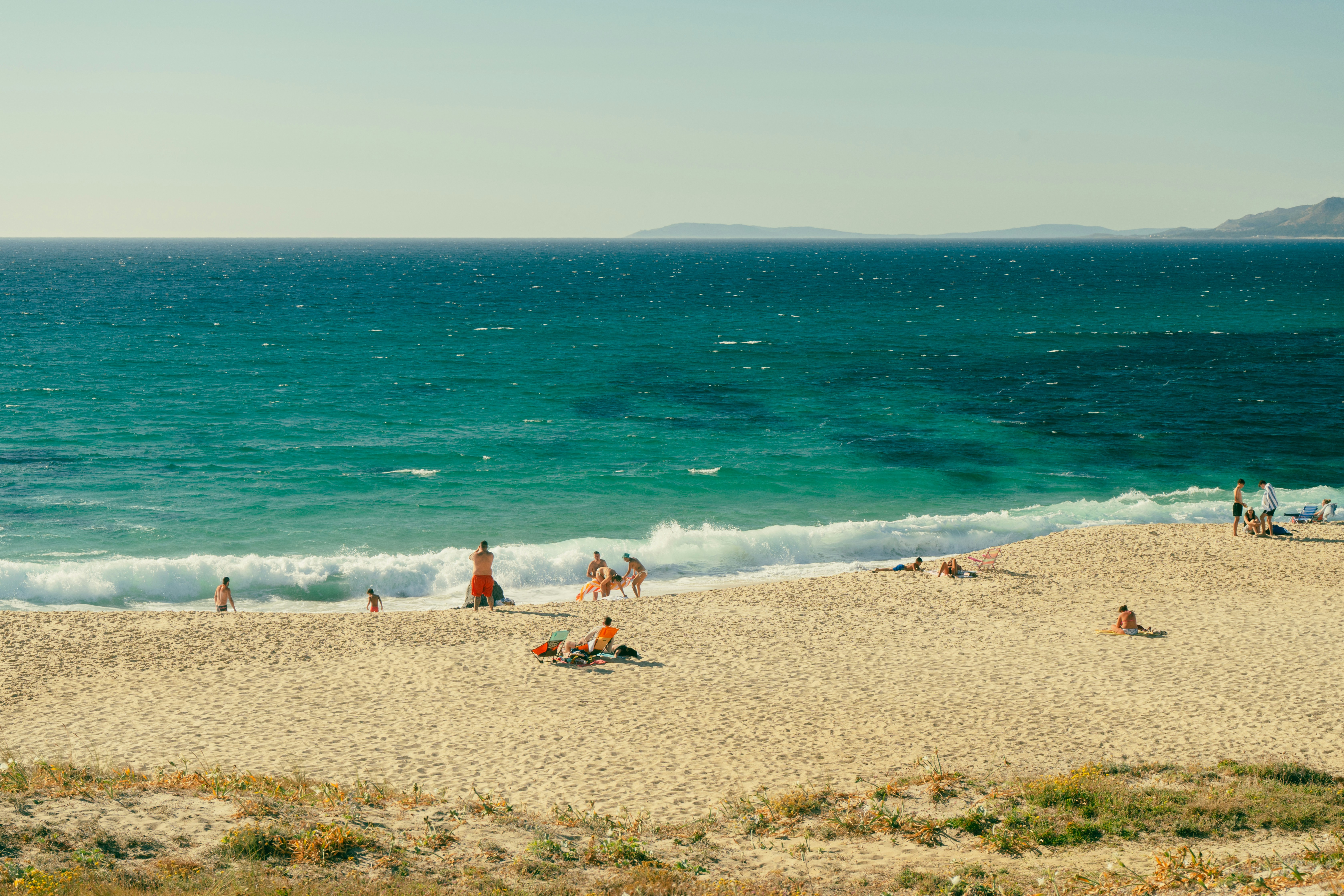 People relaxing on a sandy beach with turquoise ocean waves.