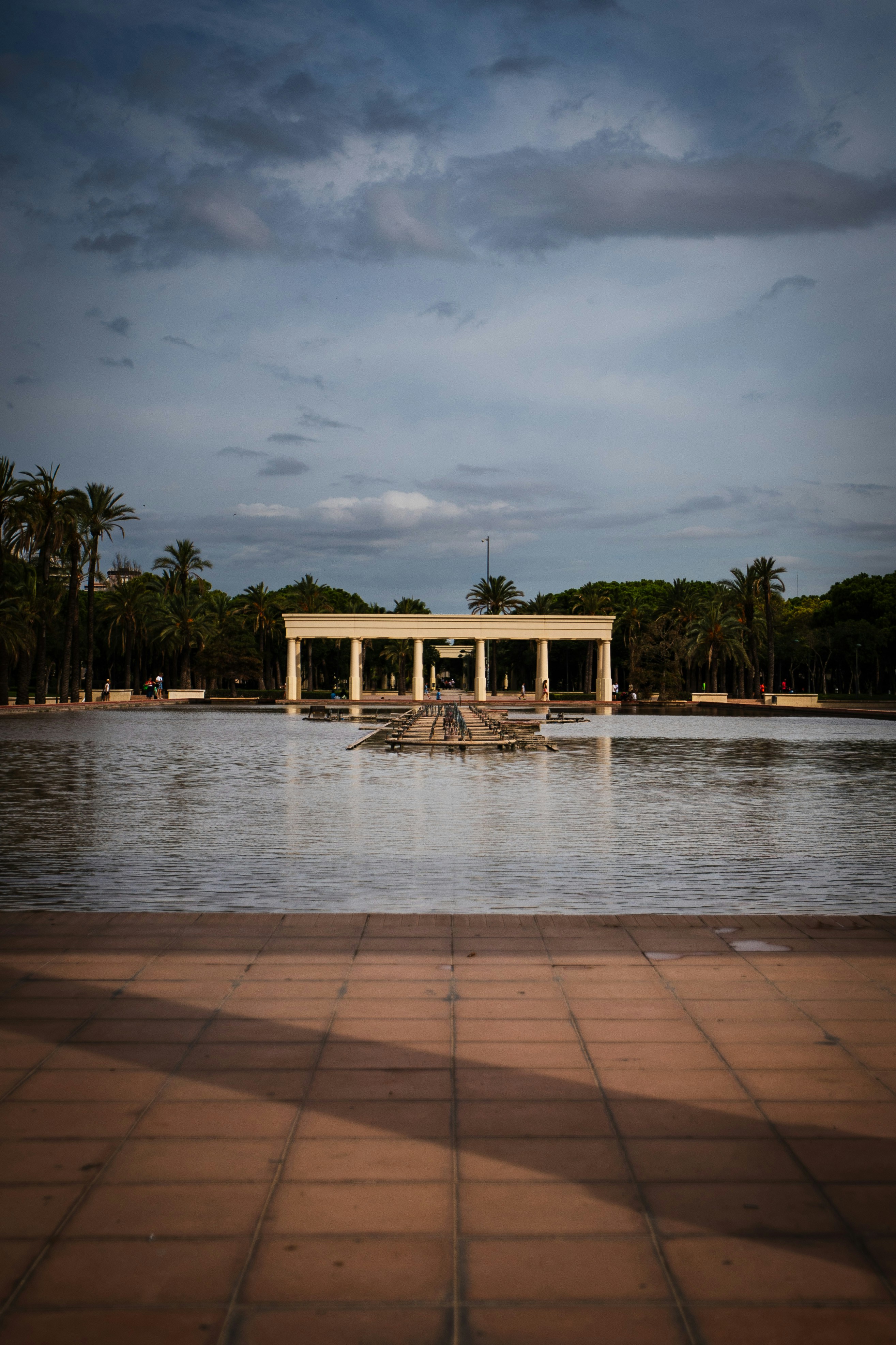Majestic structure framed by palm trees, reflecting in the calm water of a plaza. The scene captures a moment of peace in an urban environment.