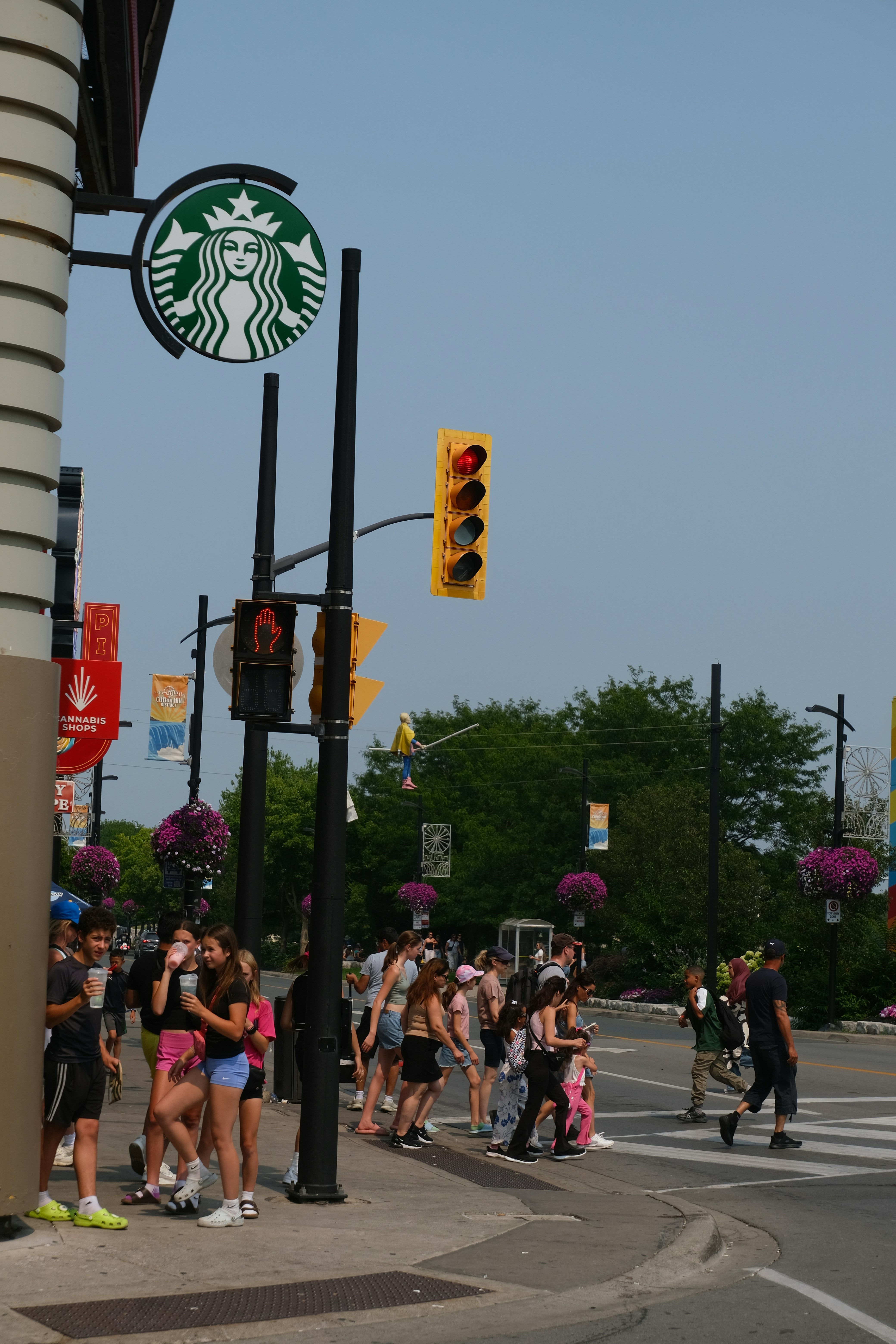 Crowd of people gathered at a busy intersection near a Starbucks, with vibrant flowers and traffic signals visible.
