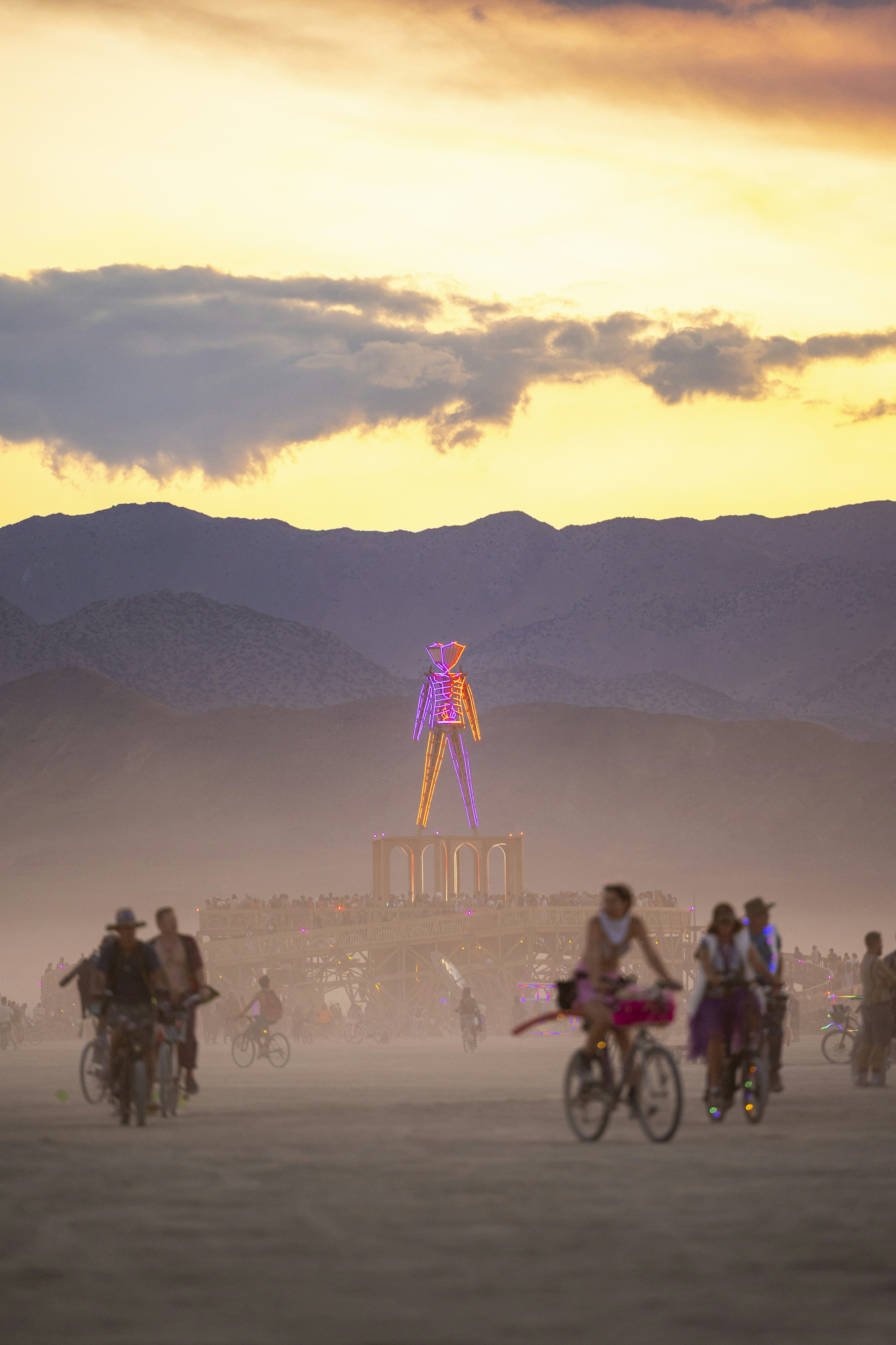 People cycle past illuminated man sculpture at sunset. photo – Free Image on Unsplash