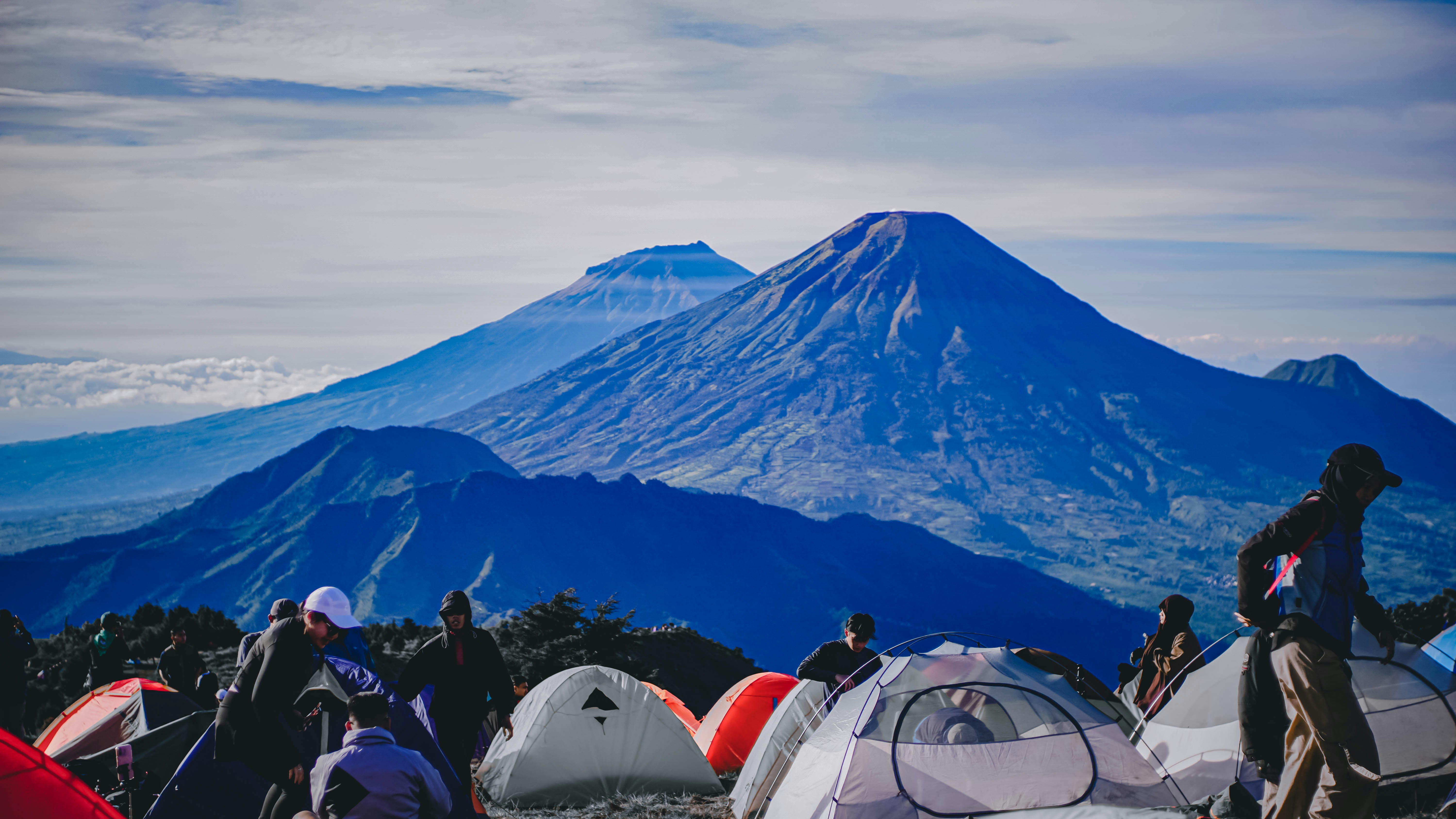 Colorful camping tents with hikers set against the stunning backdrop of Mount Sindoro and Mount Sumbing in Central Java, Indonesia. This breathtaking mountain landscape combines adventure, nature, and travel spirit, perfect for outdoor and hiking photography lovers | Campground with tents pitched on a mountain slope.