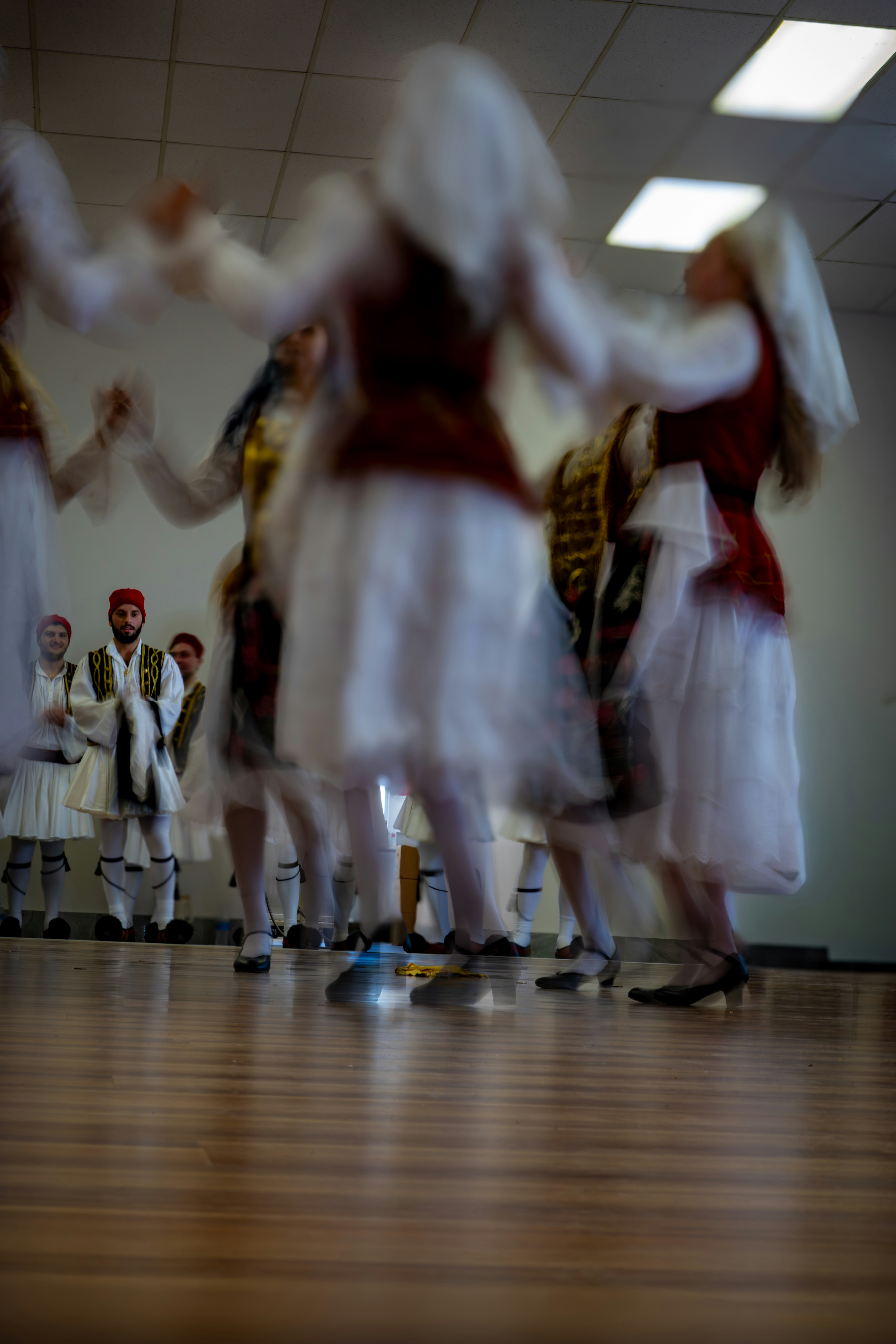 Traditional dancers in vibrant costumes performing a folk dance, captured in motion. The blurred effect emphasizes the energy and rhythm of the performance.