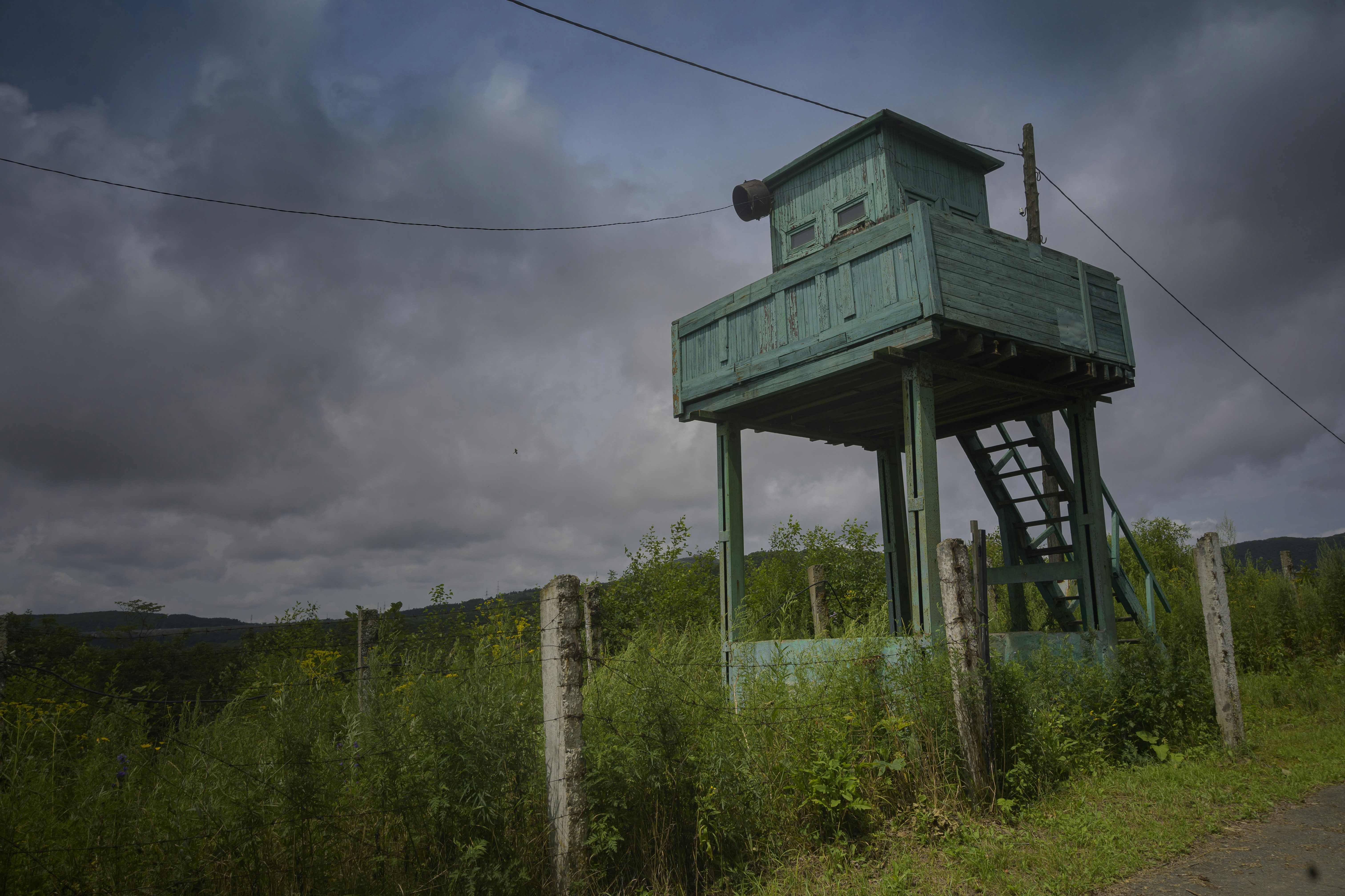 The old watchtower at the entrance to the military area. | A dilapidated green guard tower stands under a cloudy sky.